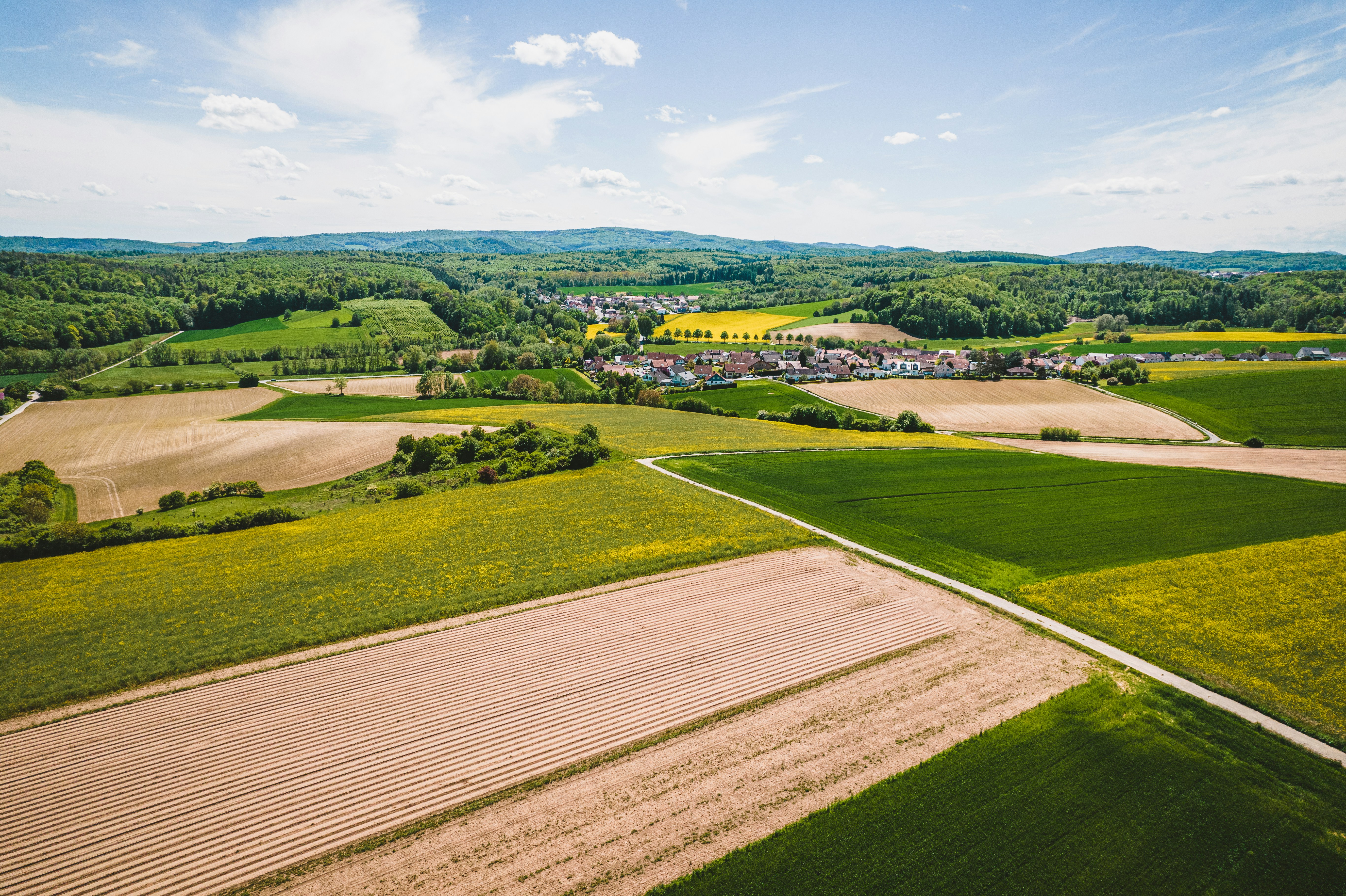 Expansive view of agricultural fields and a quaint village nestled among lush greenery and rolling hills.