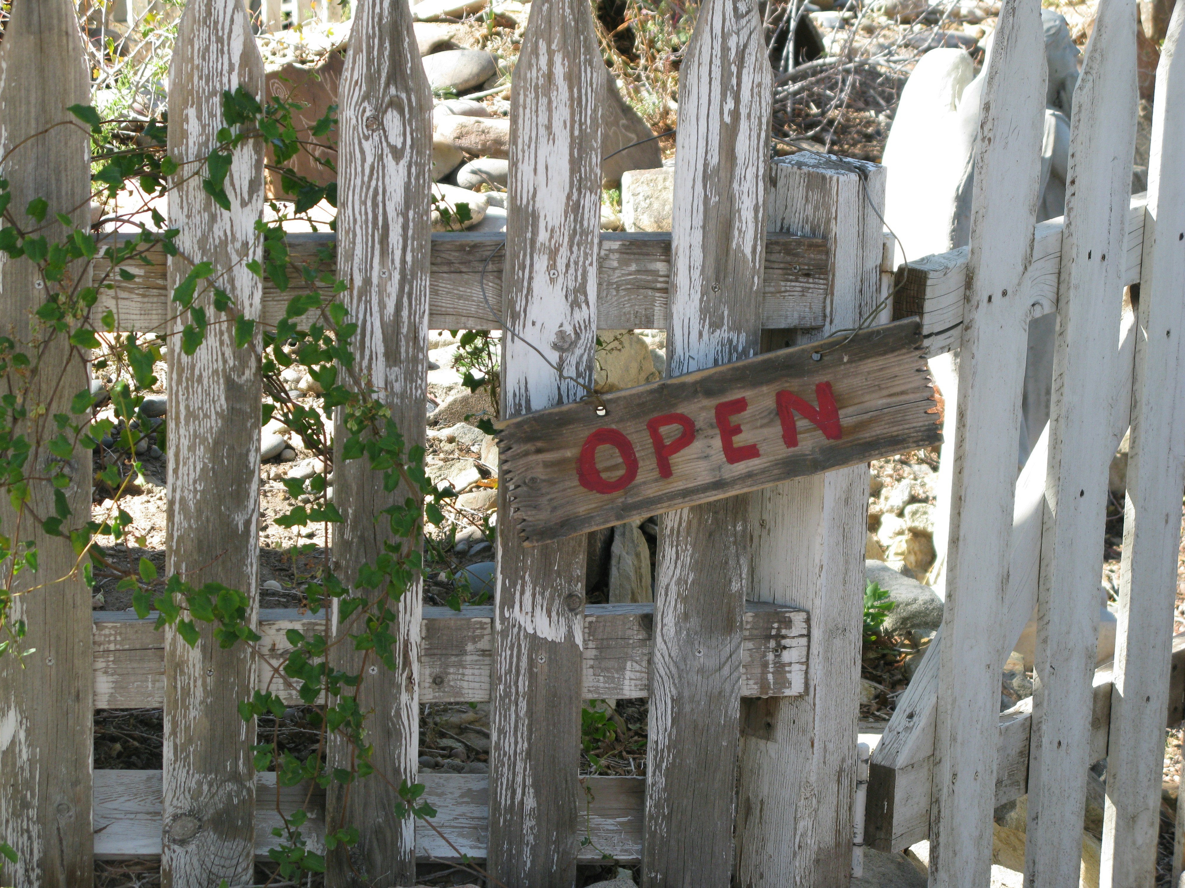 A rustic wooden fence adorned with a weathered sign reading 'OPEN,' surrounded by greenery. The scene evokes a sense of warmth and hospitality.