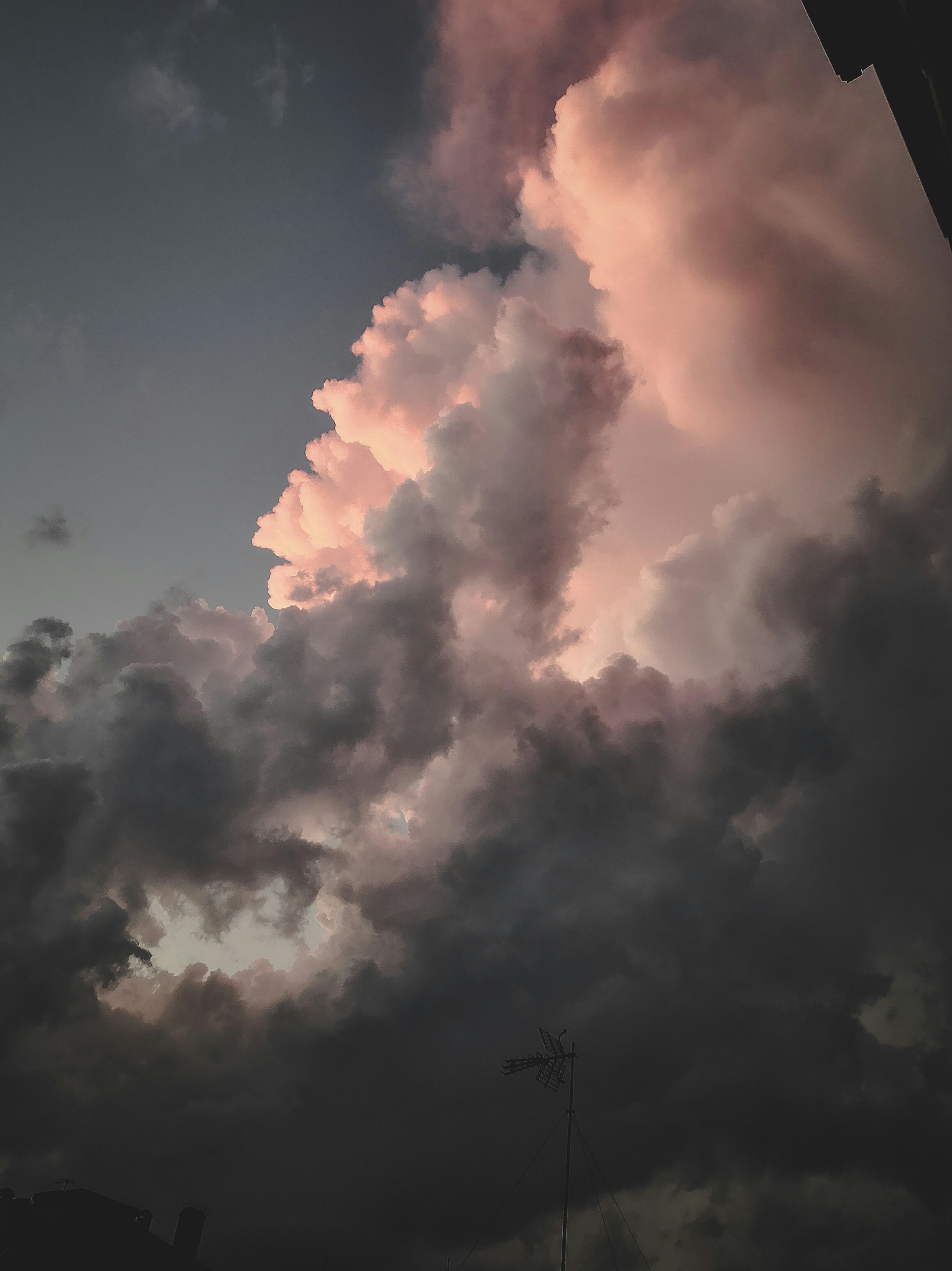 Dramatic clouds illuminated by the setting sun, creating a dynamic interplay of light and shadow. An antenna peeks from the bottom, adding a human element to the natural spectacle.