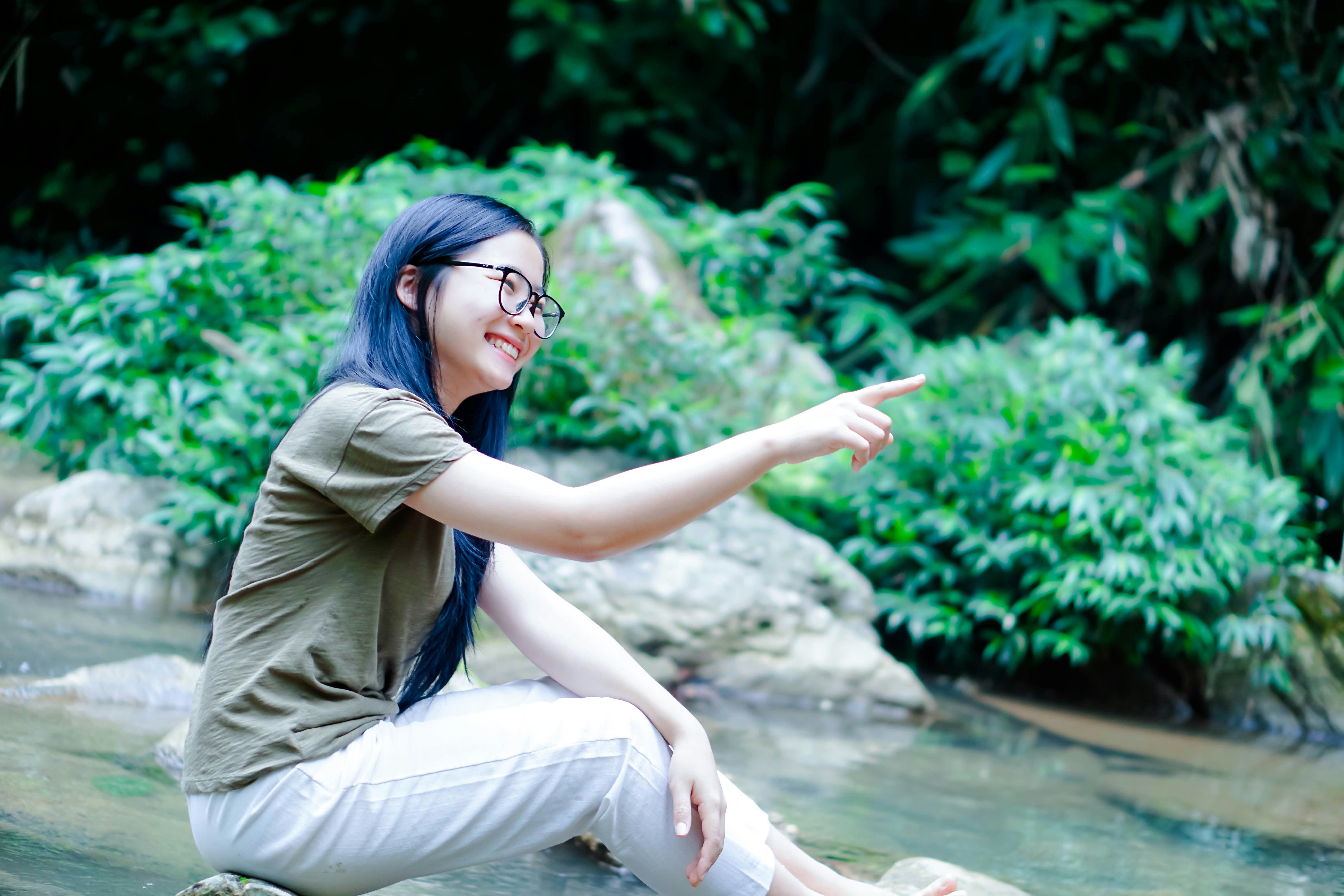 A woman sitting on a rock pointing at something photo – Free Woman ...
