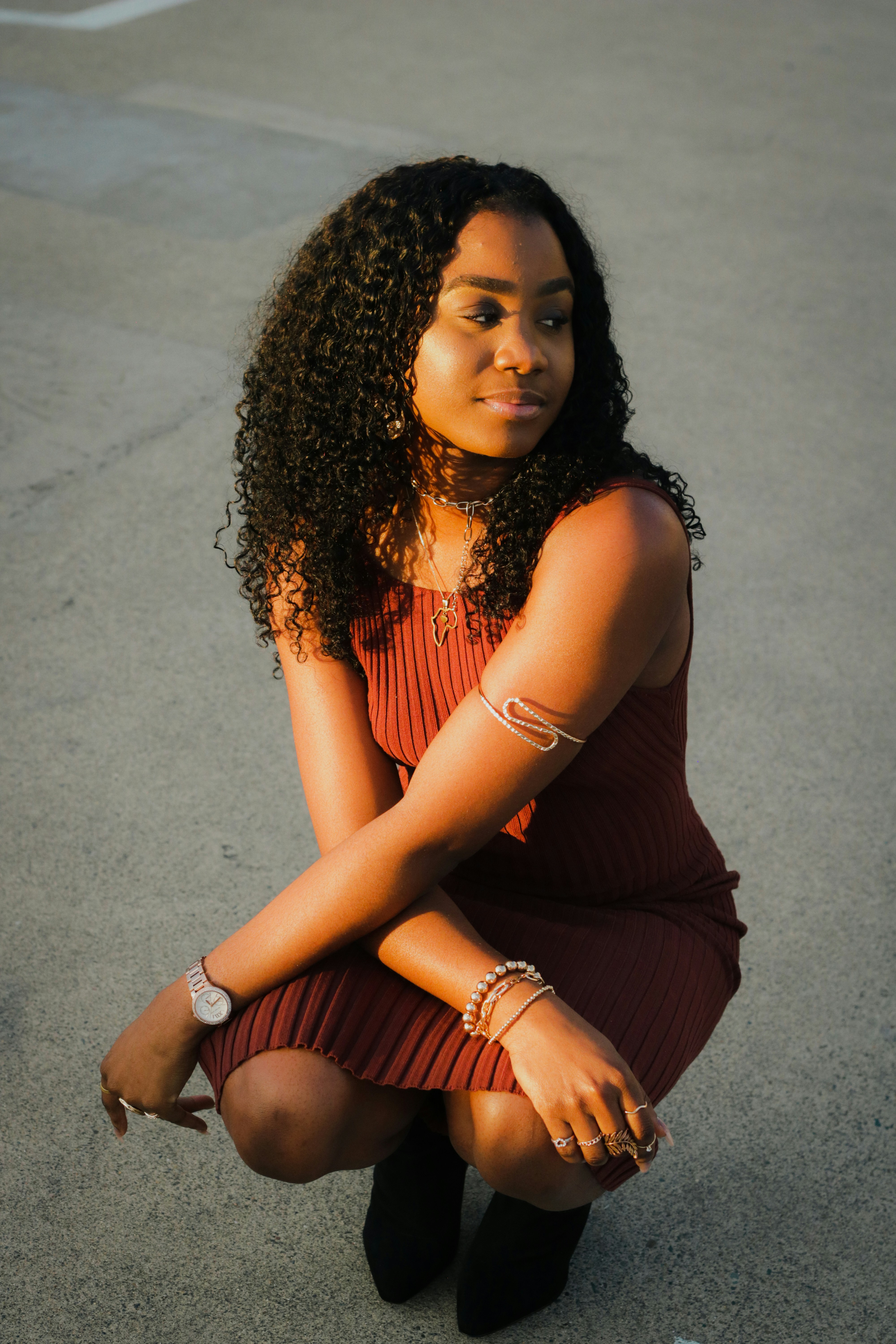 Woman in a red dress crouching on a sunlit pavement.