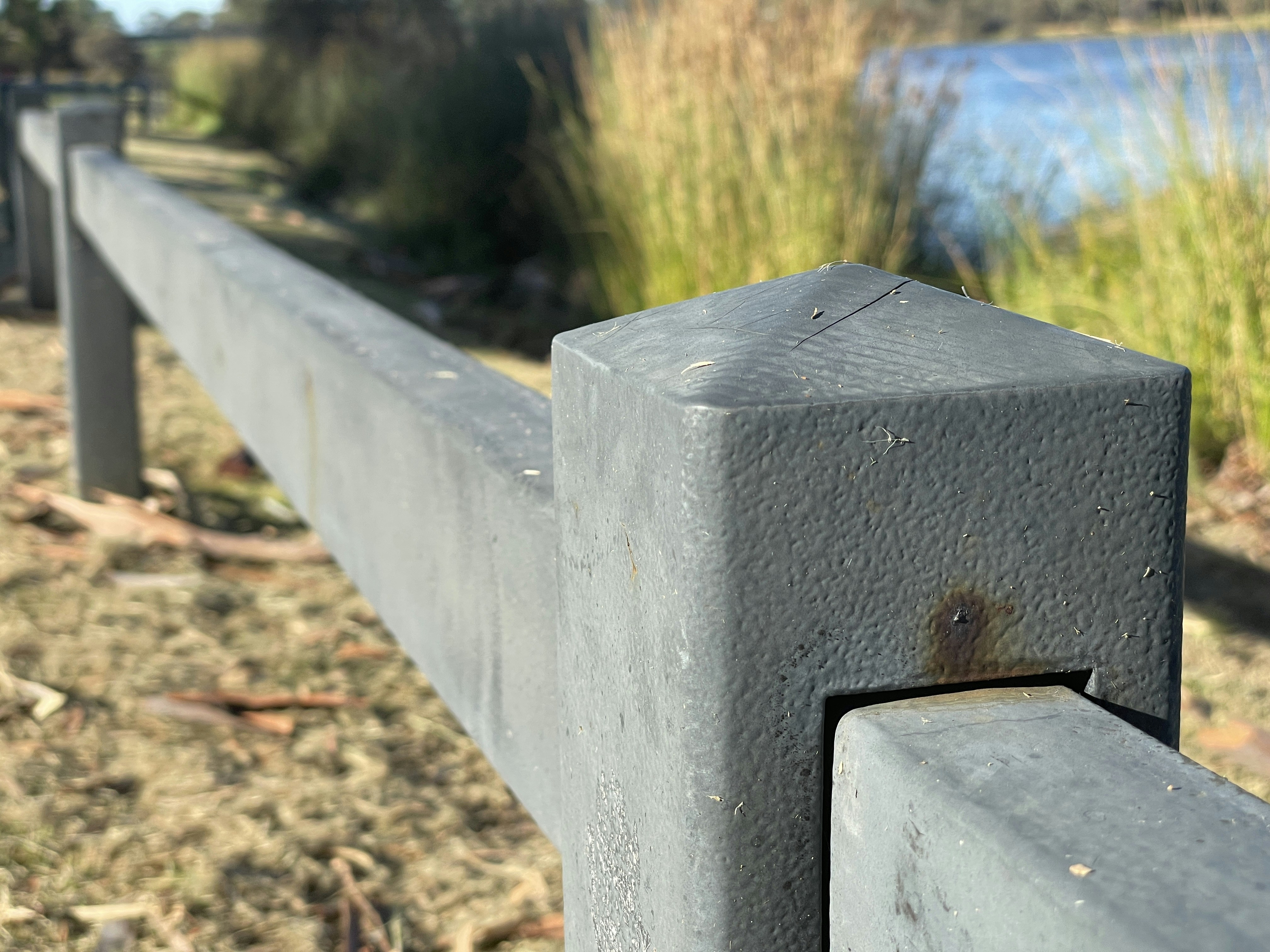 Rusted Rail in Focus: A Close-Up of Steel and Sunlit Riverside