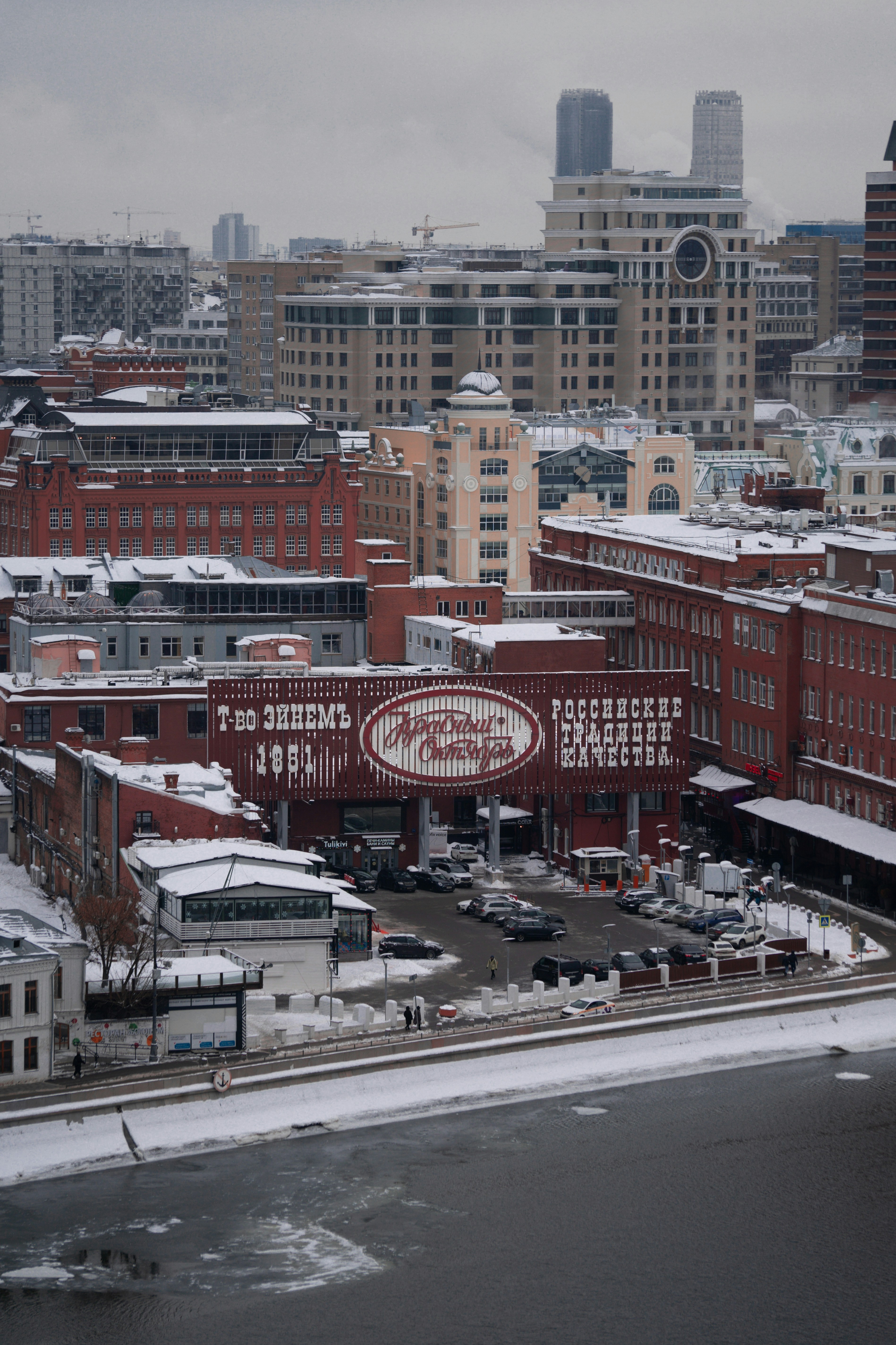 Historic red-brick buildings contrasted against a contemporary skyline, with snow covering the ground and a river flowing nearby.