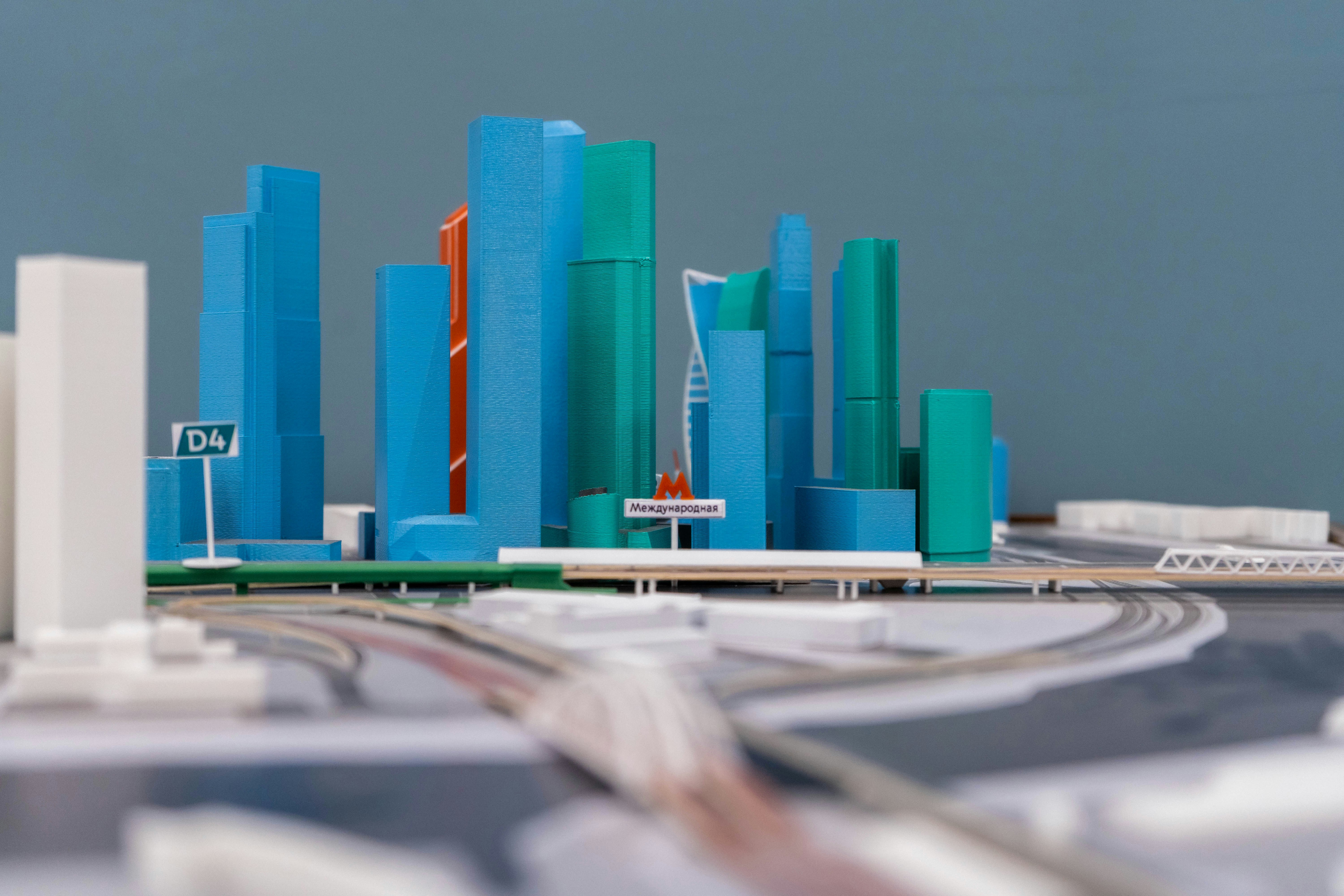 Colorful architectural model showcasing a modern city skyline with various skyscrapers and a prominent sign. A blend of blue and green structures creates a dynamic visual narrative.