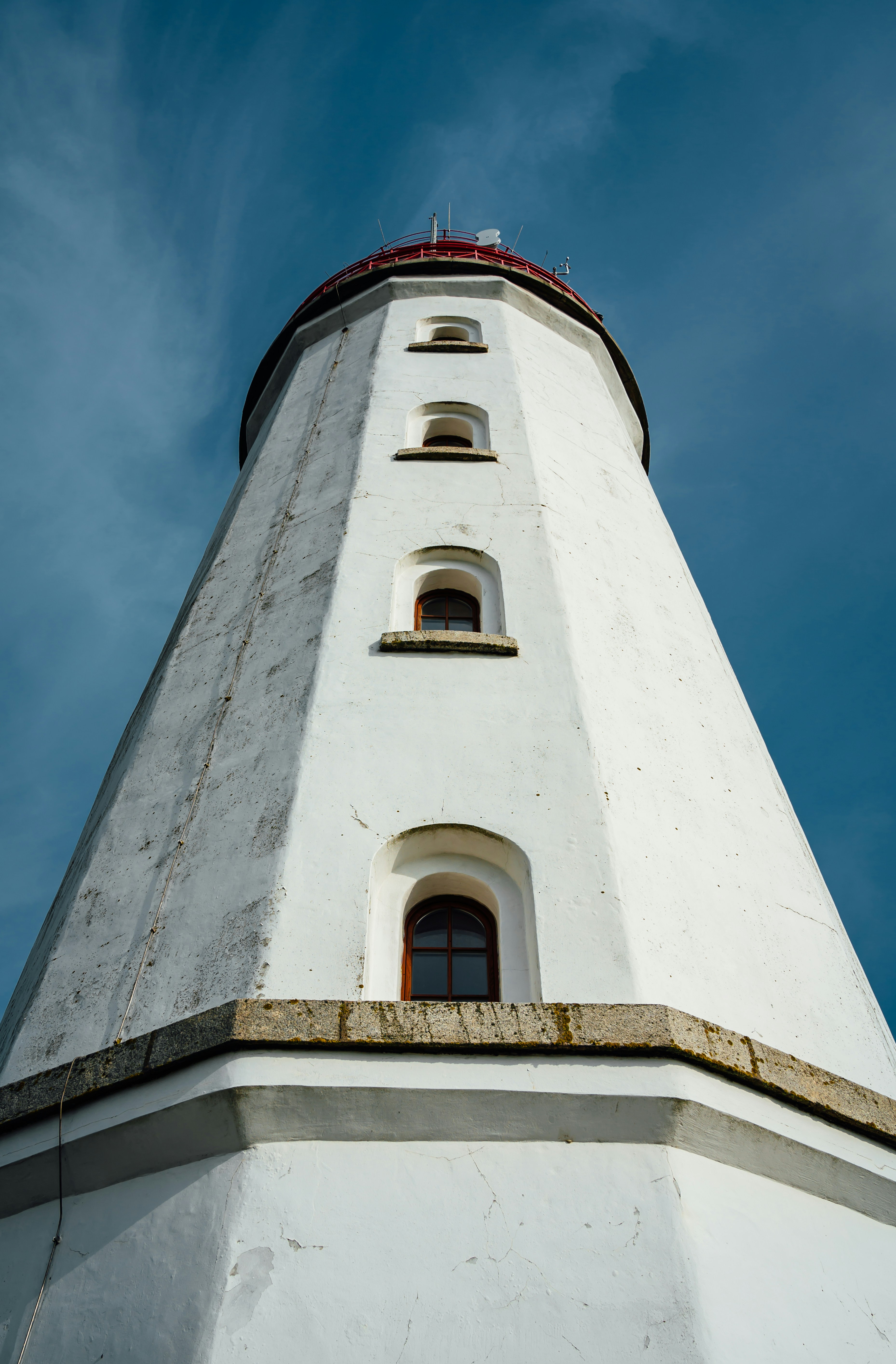 A towering lighthouse rises against a clear blue sky, showcasing its architectural details and vibrant red top.