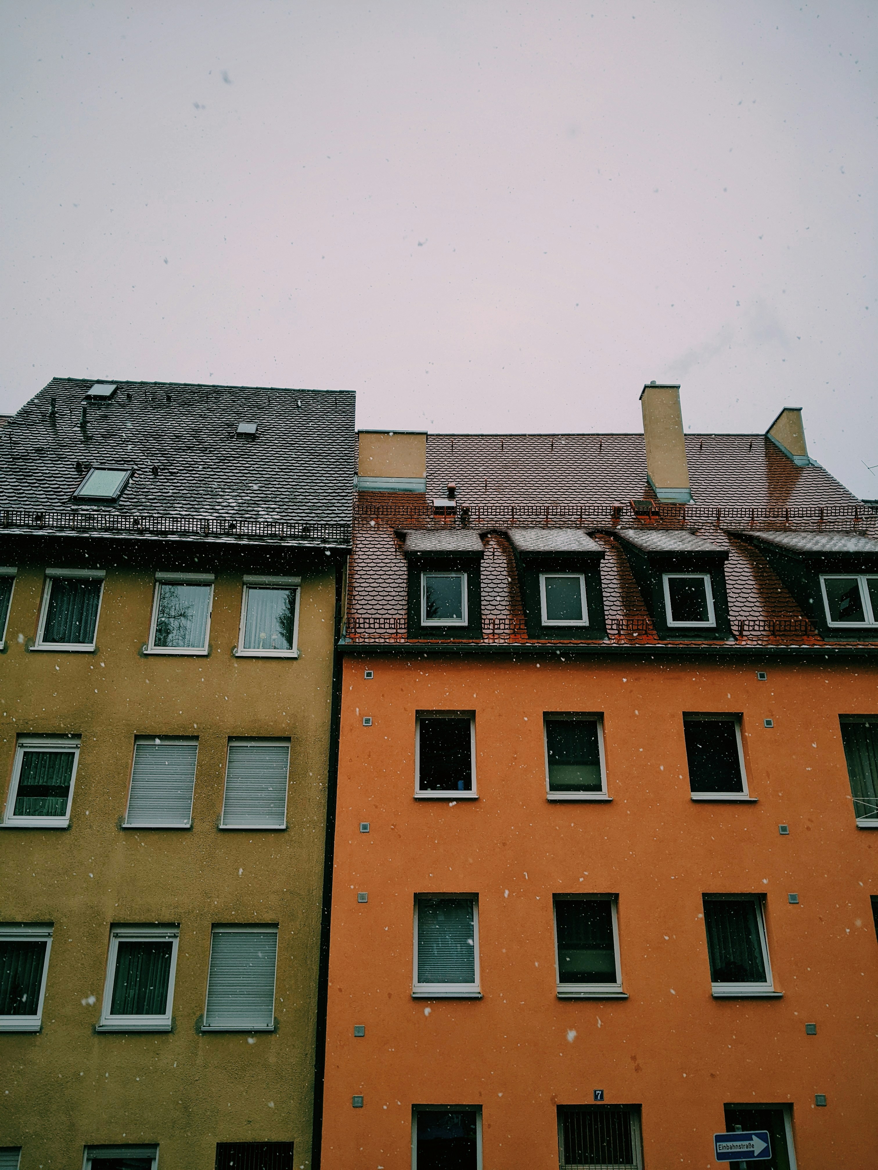 Colorful apartment buildings under a snowy sky, showcasing a blend of architectural styles. Snowflakes gently descend, adding a serene atmosphere.