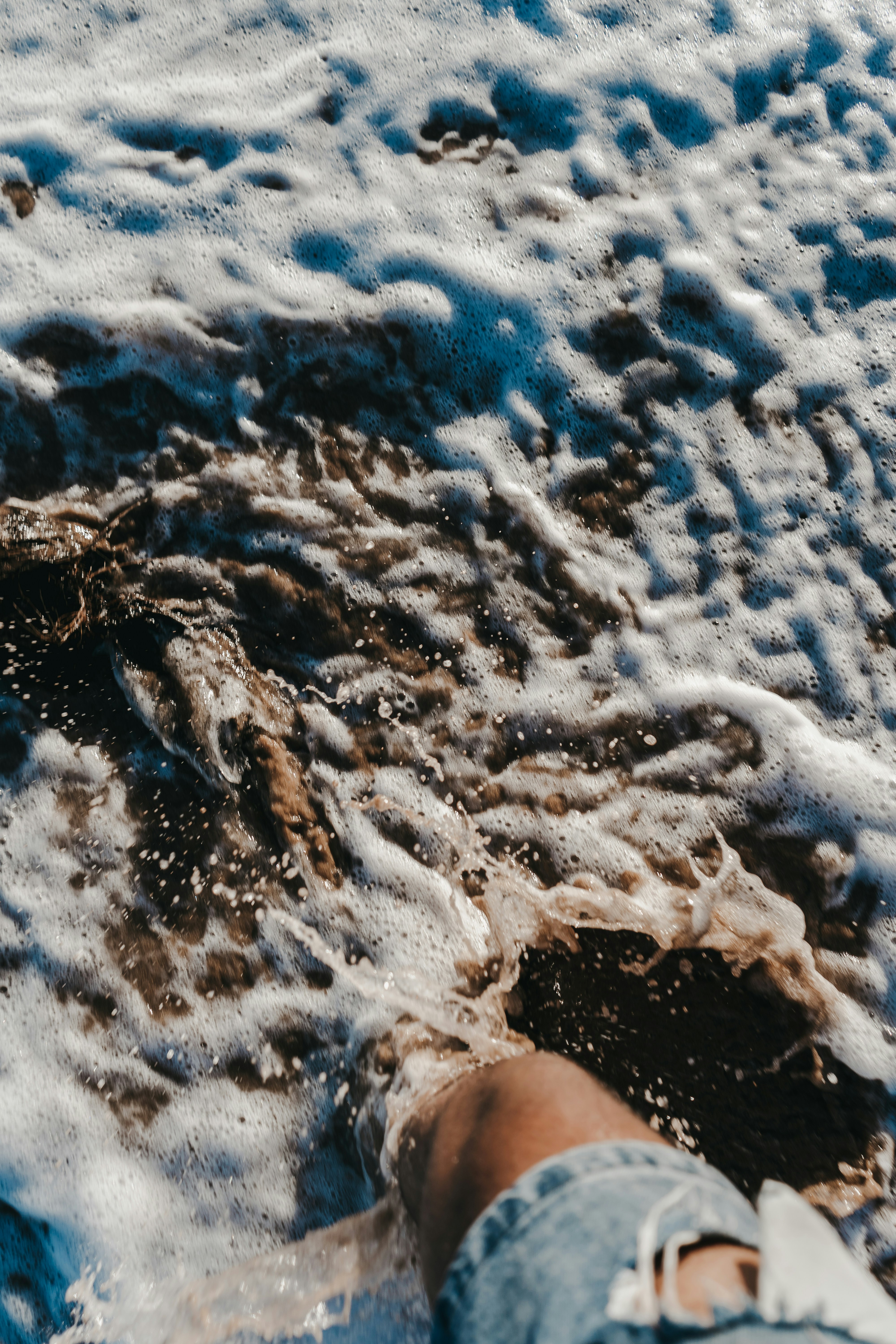 Foam-Touched Shorestep: a close-up of a denim-clad leg in surf