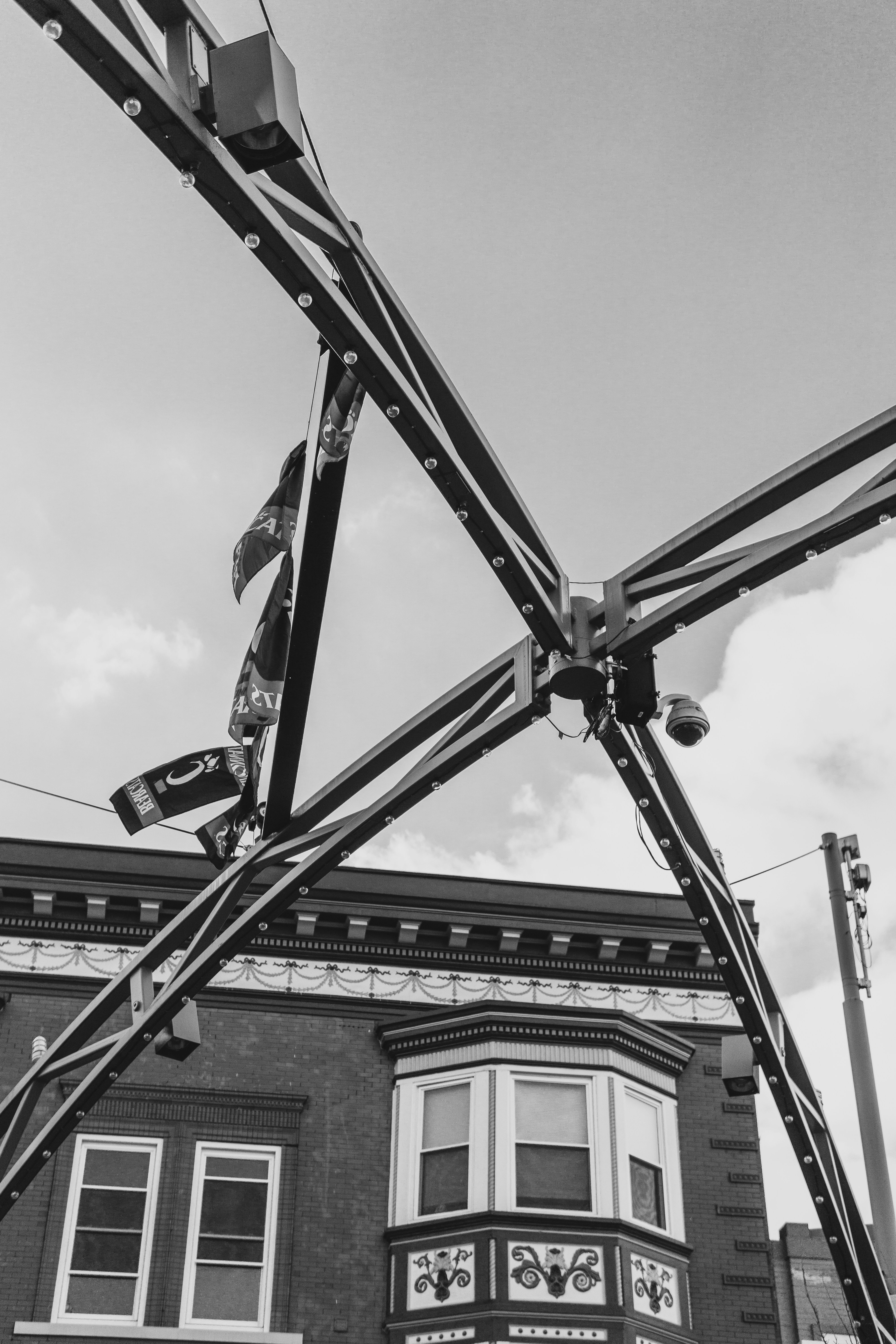 Black and white photo of intersecting metal beams above a building facade with intricate window designs.
