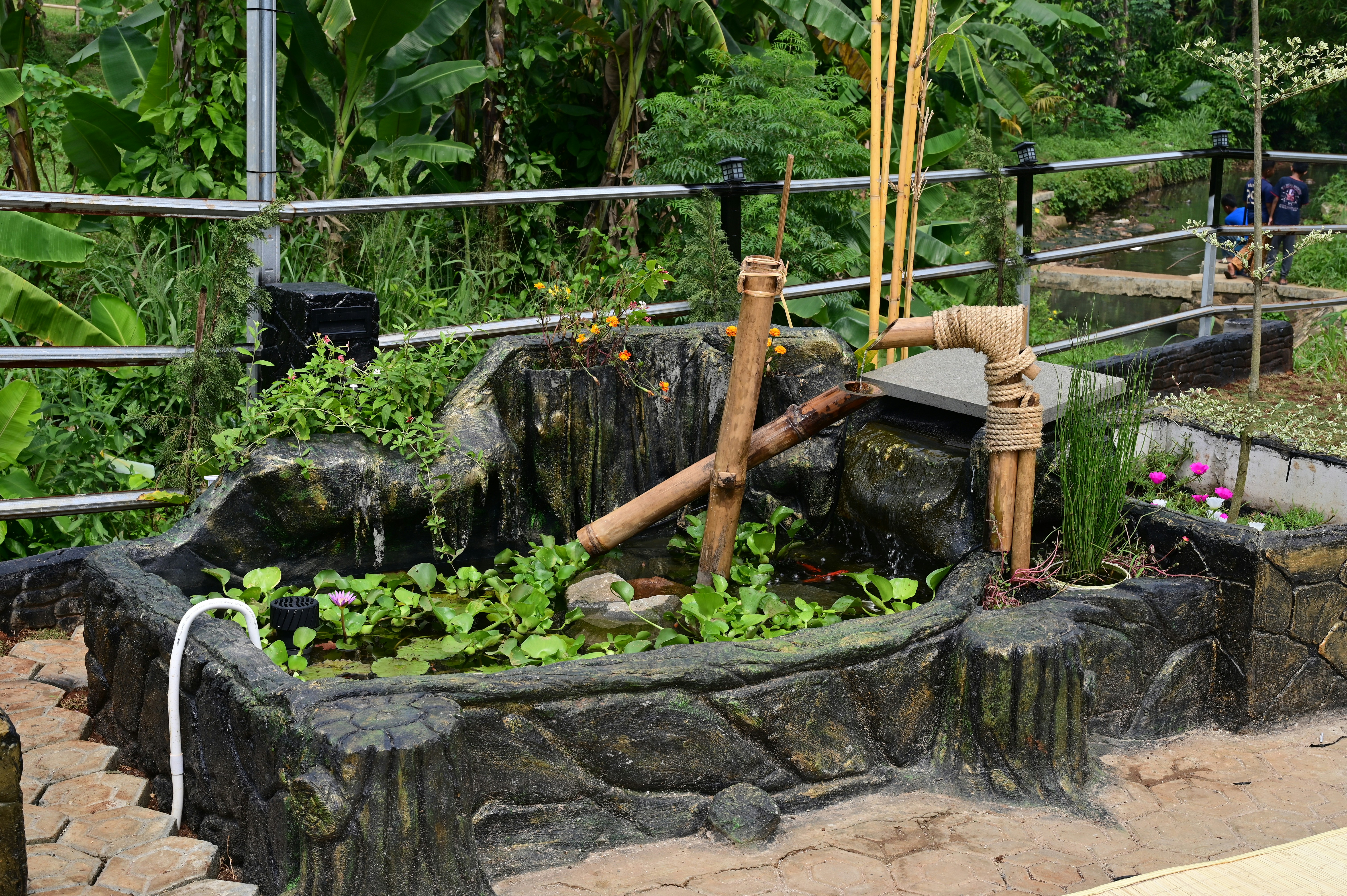 Bamboo Spout Over a Lush Rock Pond with Water Lilies