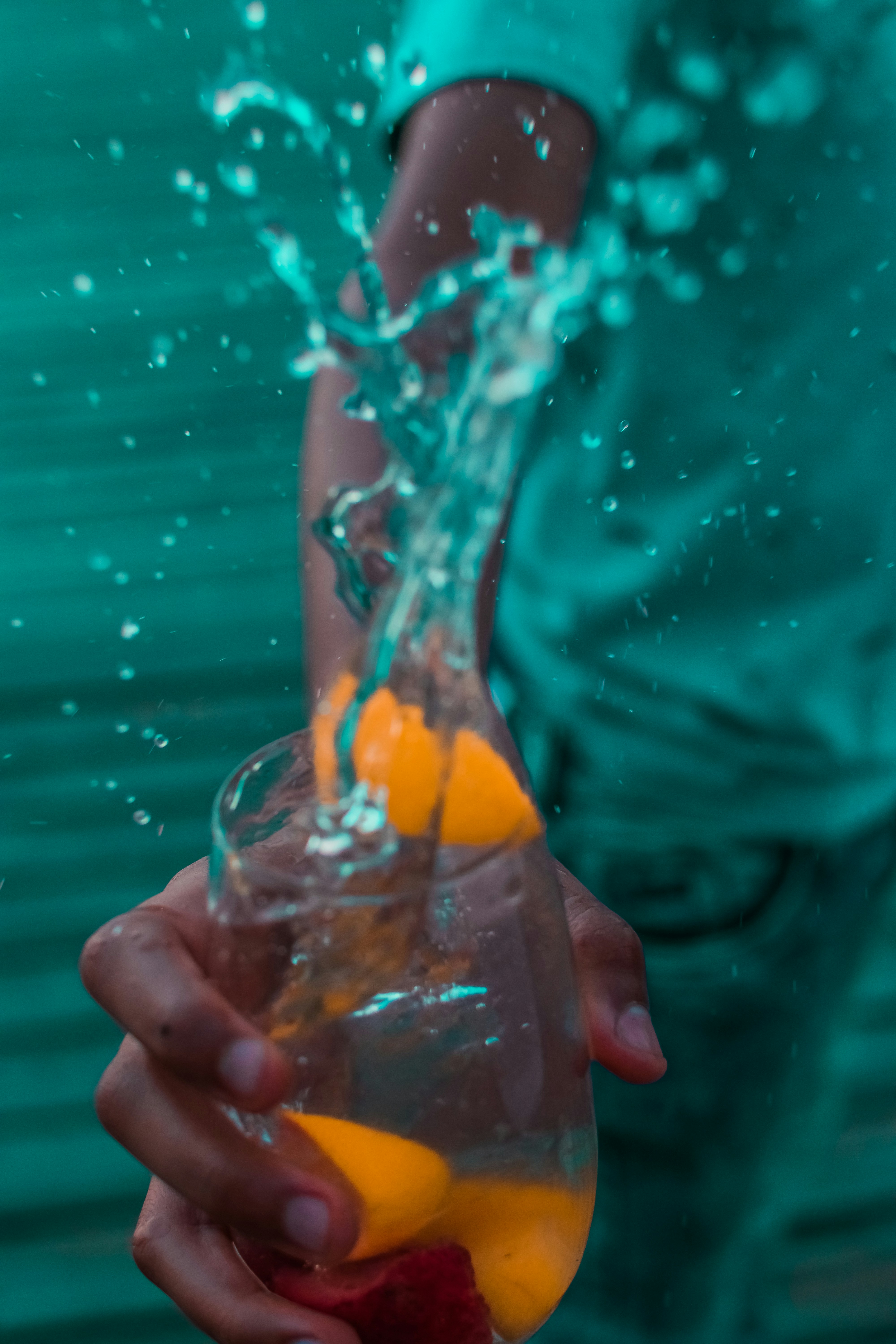 A hand holding a glass bottle filled with water and citrus fruits, as droplets splash around, emphasizing a lively summer vibe.