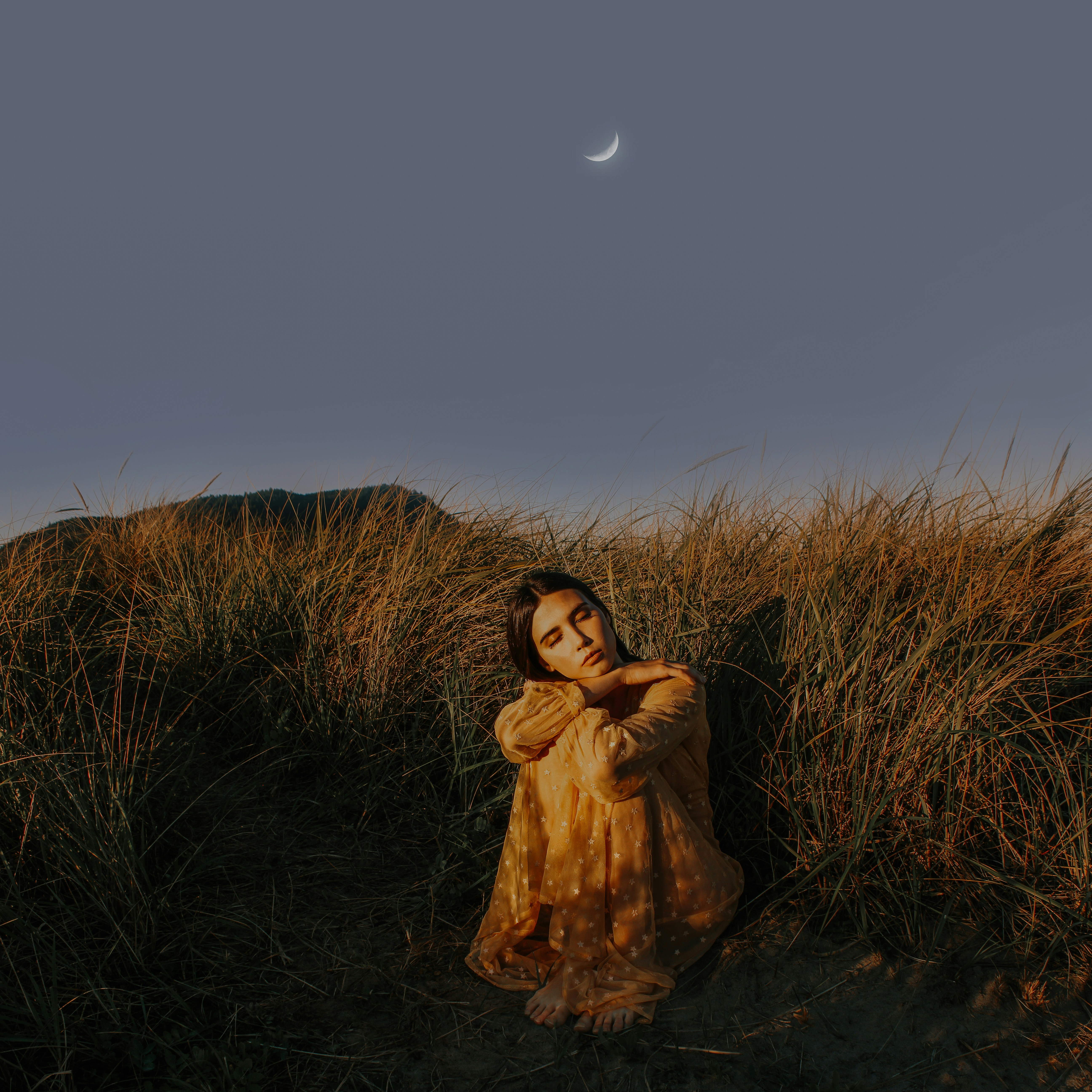 Woman in yellow dress sitting on the beach under crescent moon