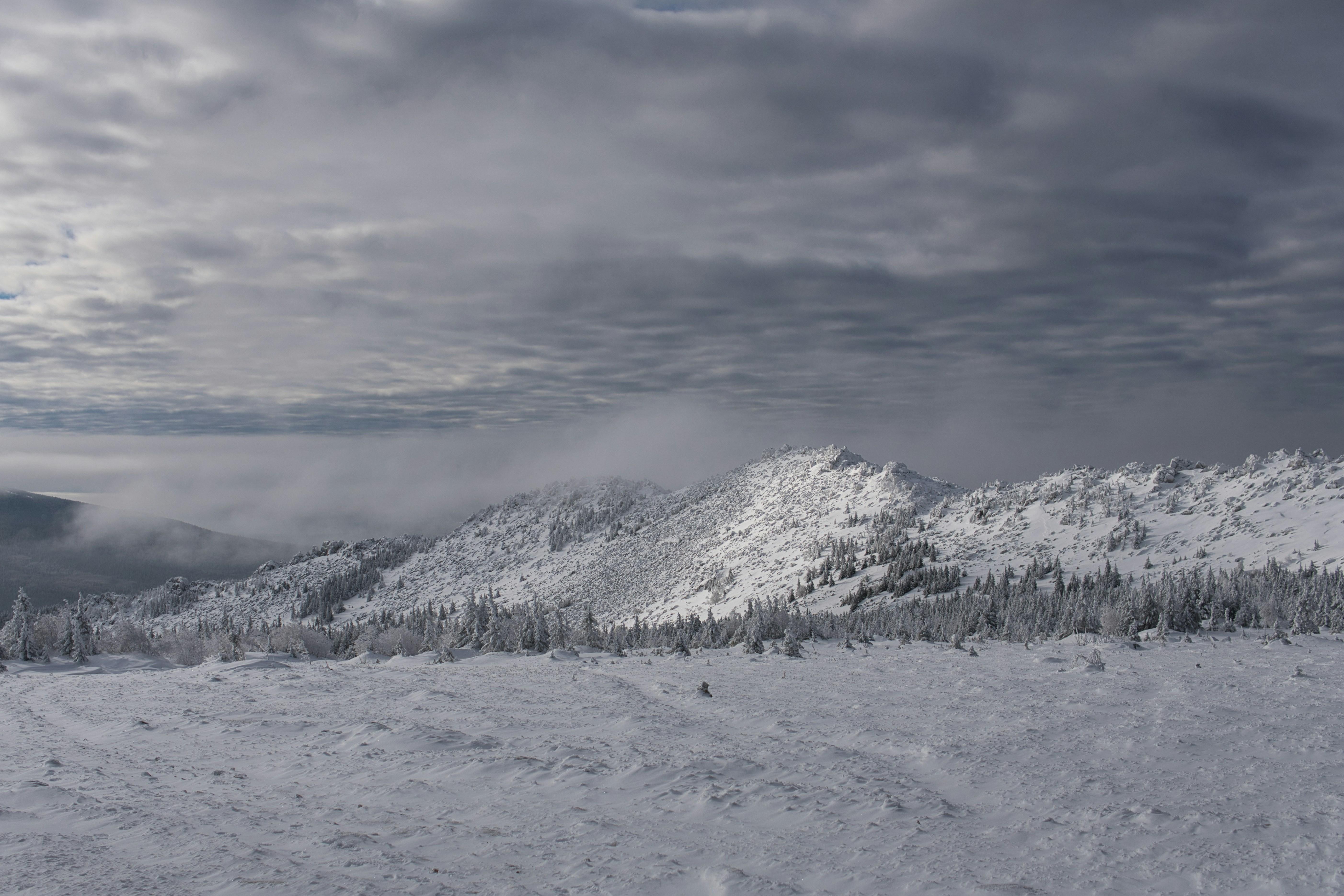 Snow-covered mountains shrouded in mist under a dramatic sky, showcasing the serene beauty of a winter landscape.
