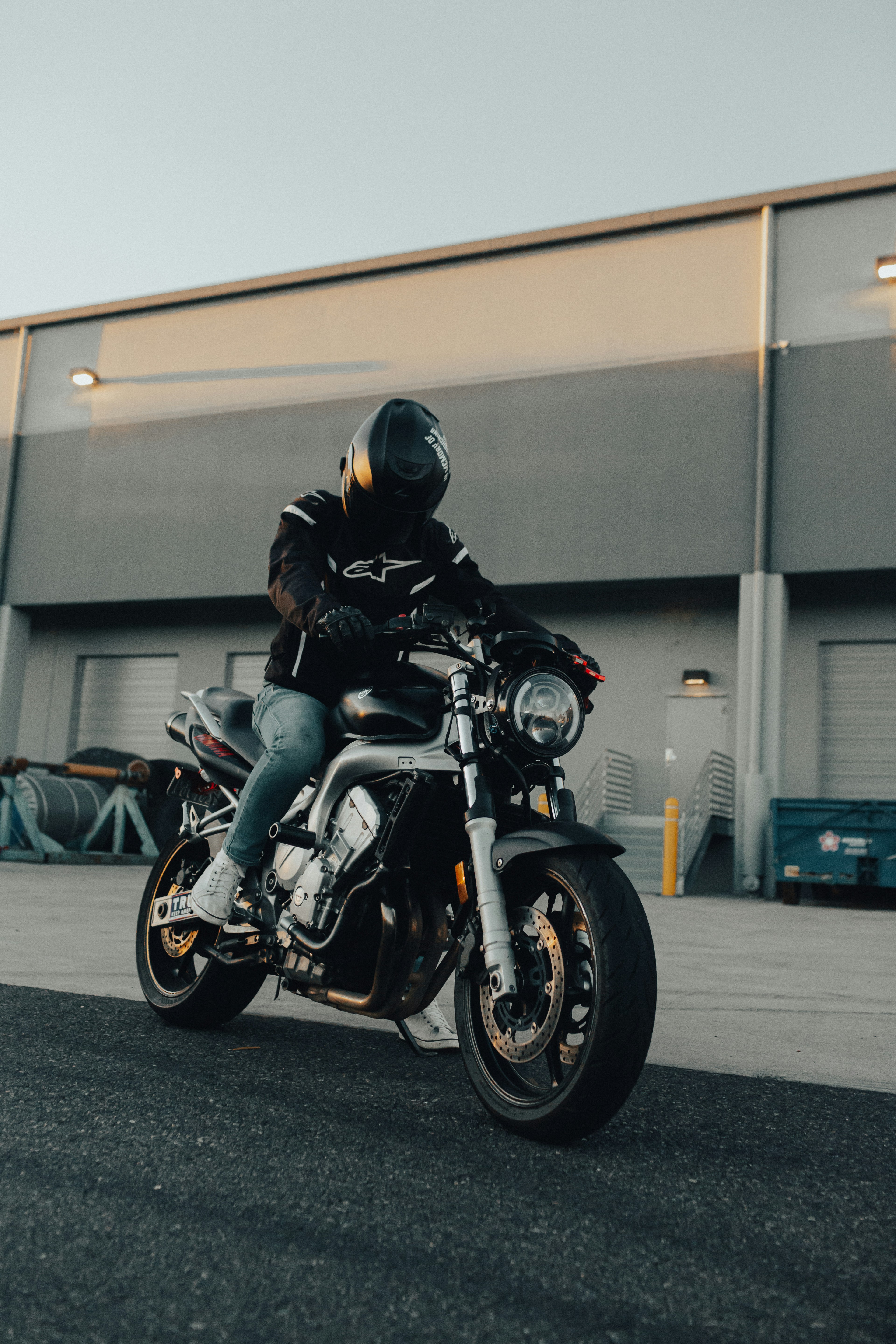A man riding a motorcycle down a street next to a building photo – Free ...