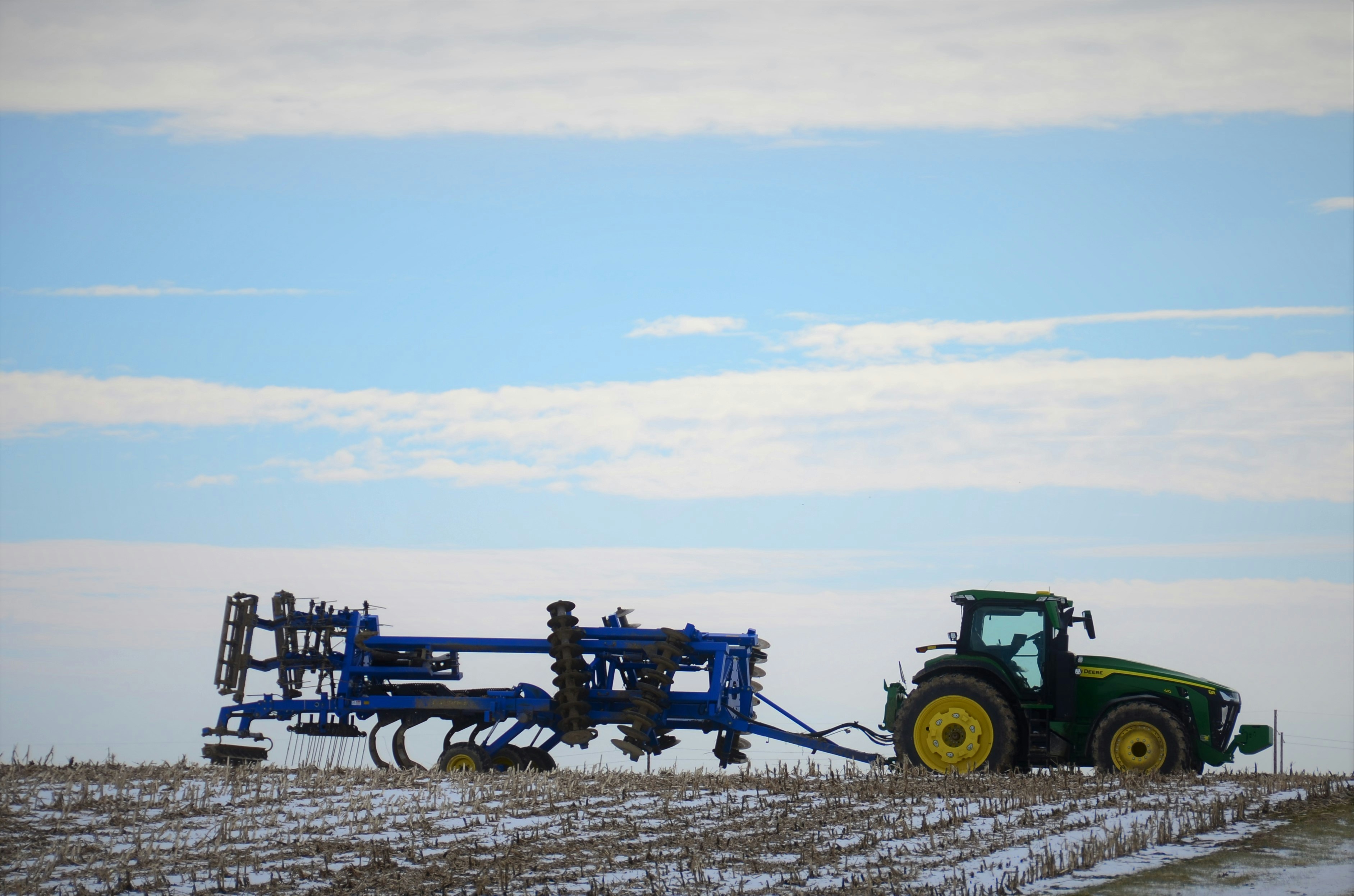 A tractor is pulling a plow across a snowy field photo – Free Blue ...