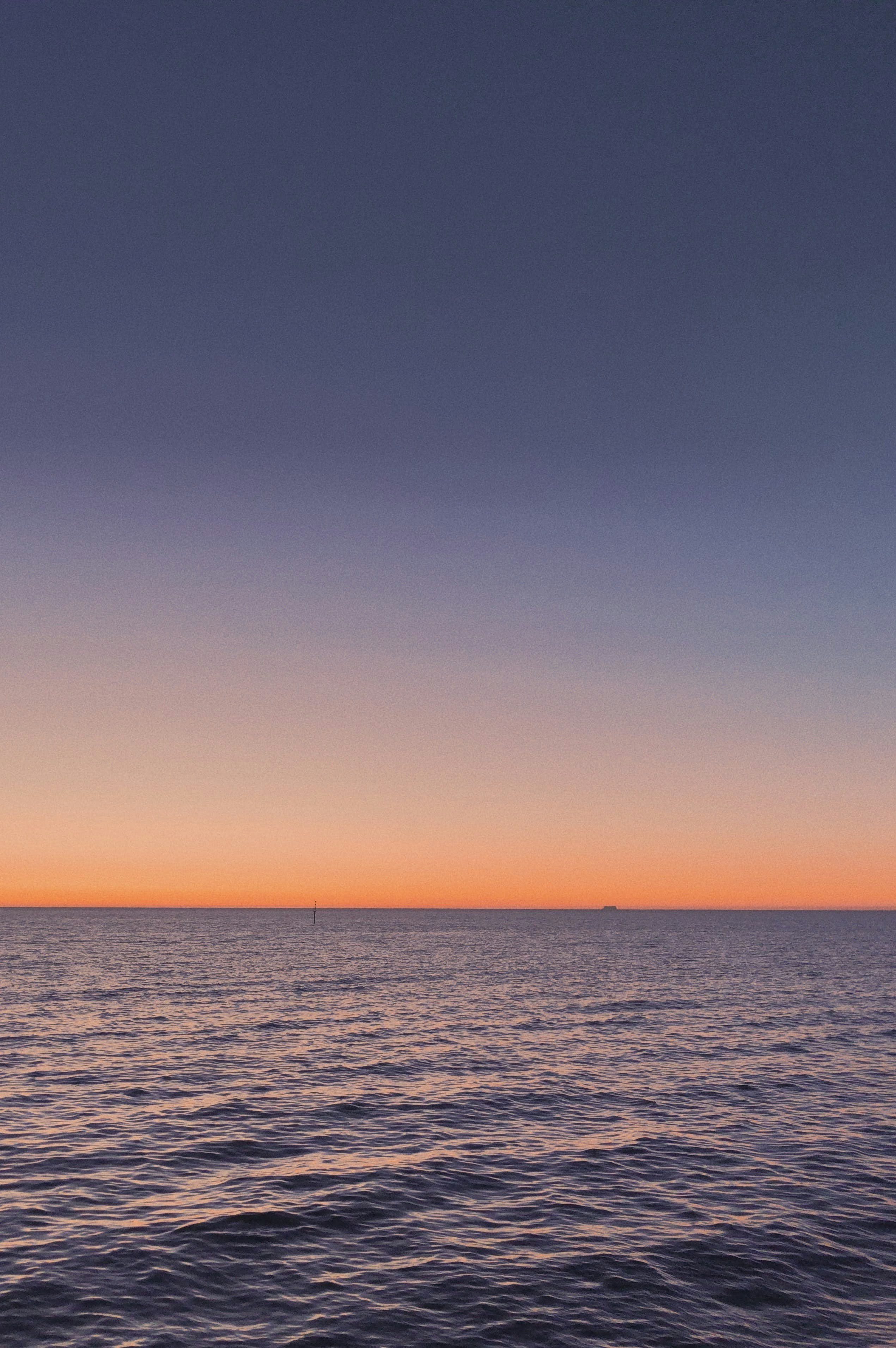 Gentle waves reflect the soft hues of twilight as the sky transitions from blue to orange over the calm sea.