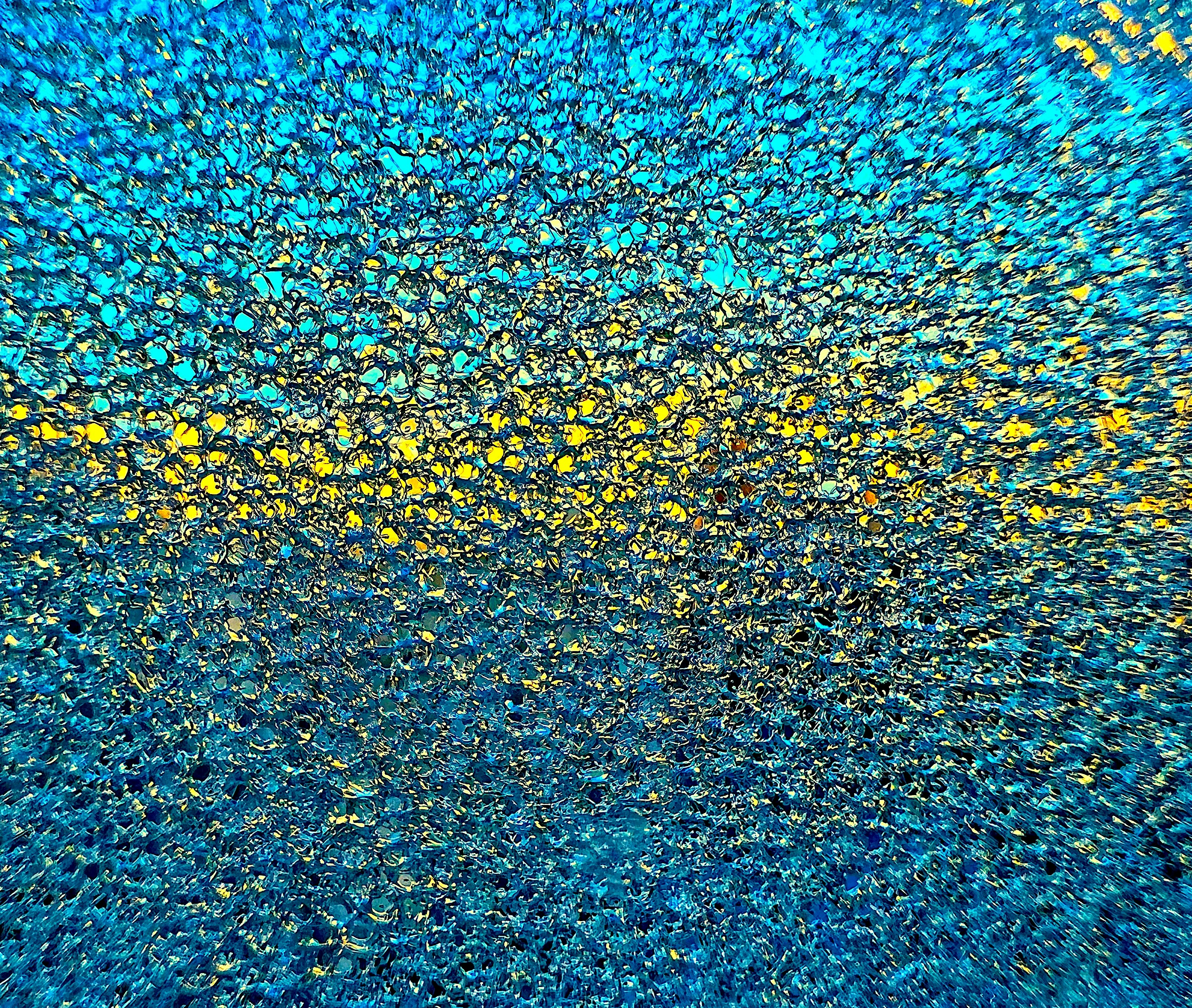 Abstract pattern of droplets on a surface, blending vibrant shades of blue and yellow. The interplay of light creates a dynamic visual texture.