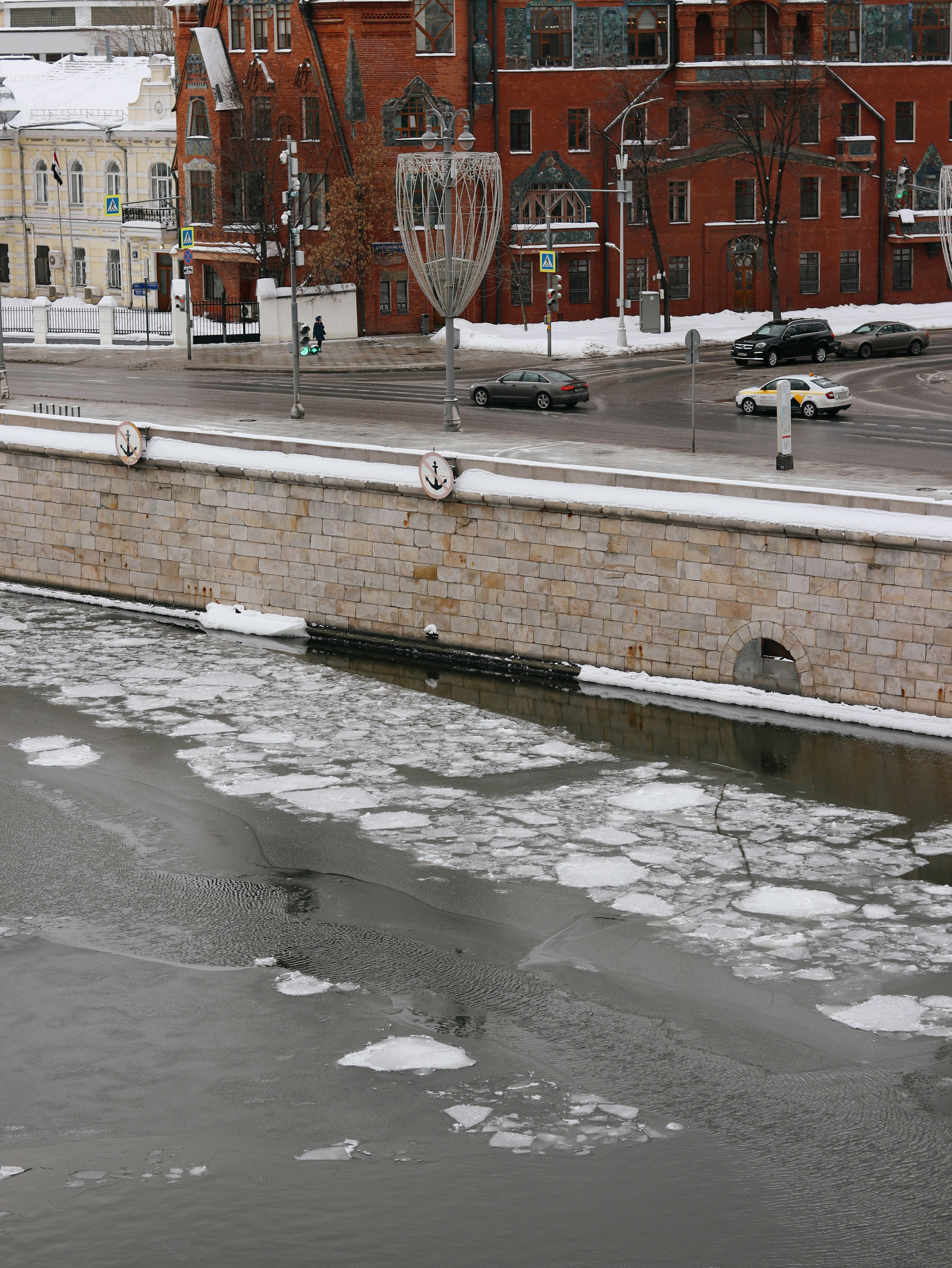 Historic buildings line the snowy riverbank, while patches of ice float on the water's surface, creating a serene winter scene.