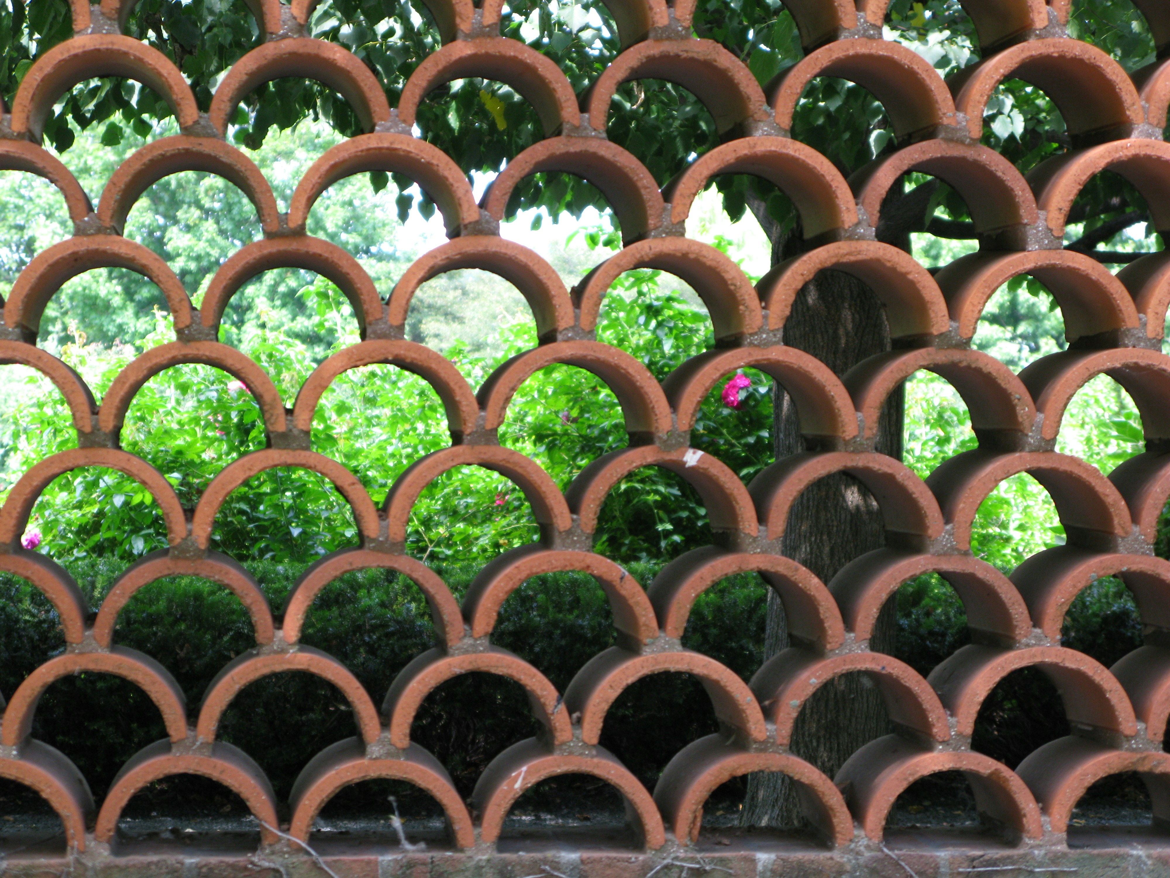 Terracotta tiles arranged in a rhythmic pattern frame a lush garden backdrop, showcasing vibrant greenery and colorful blooms.