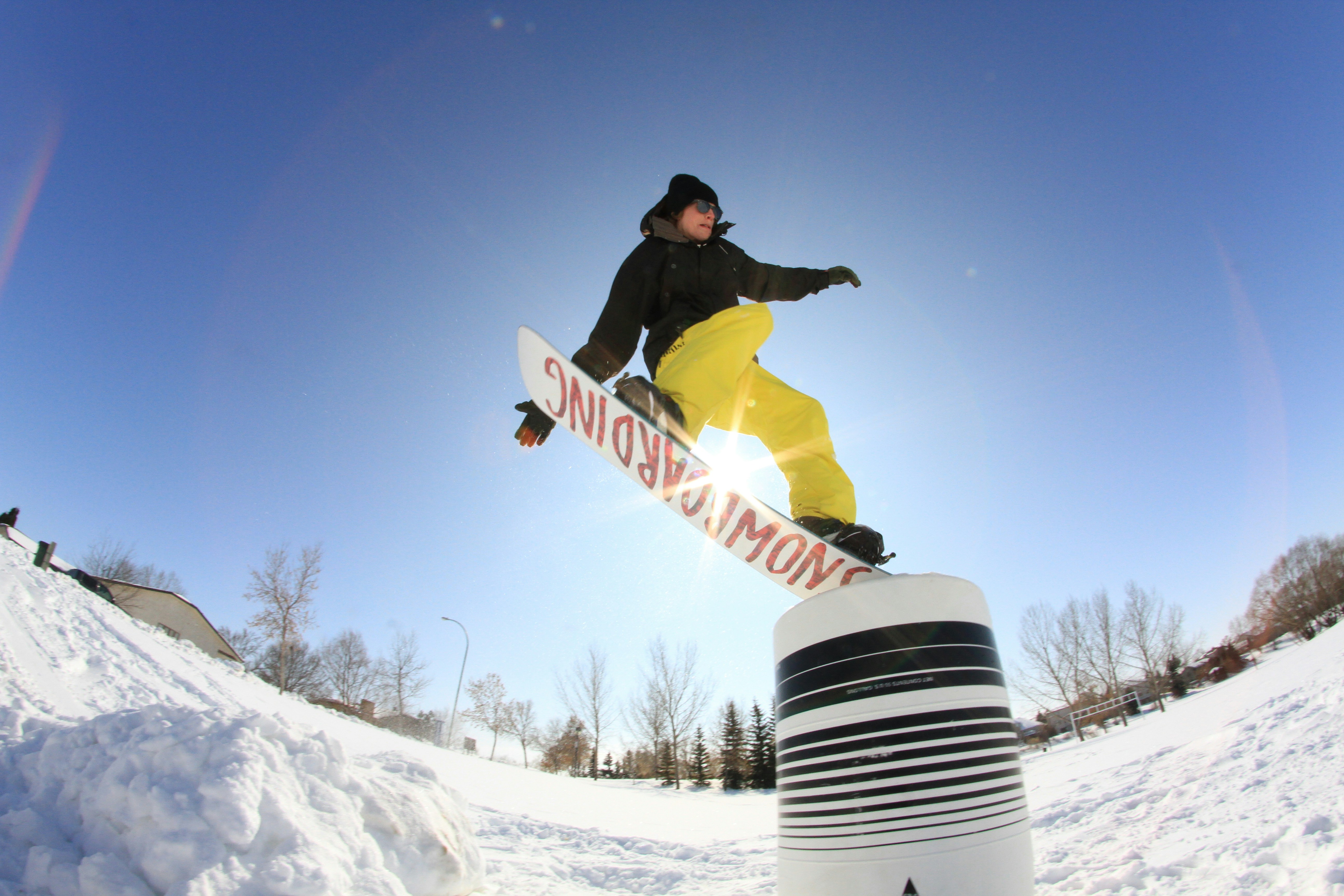 Snowboarder mid-air over a foam ramp against a bright blue sky