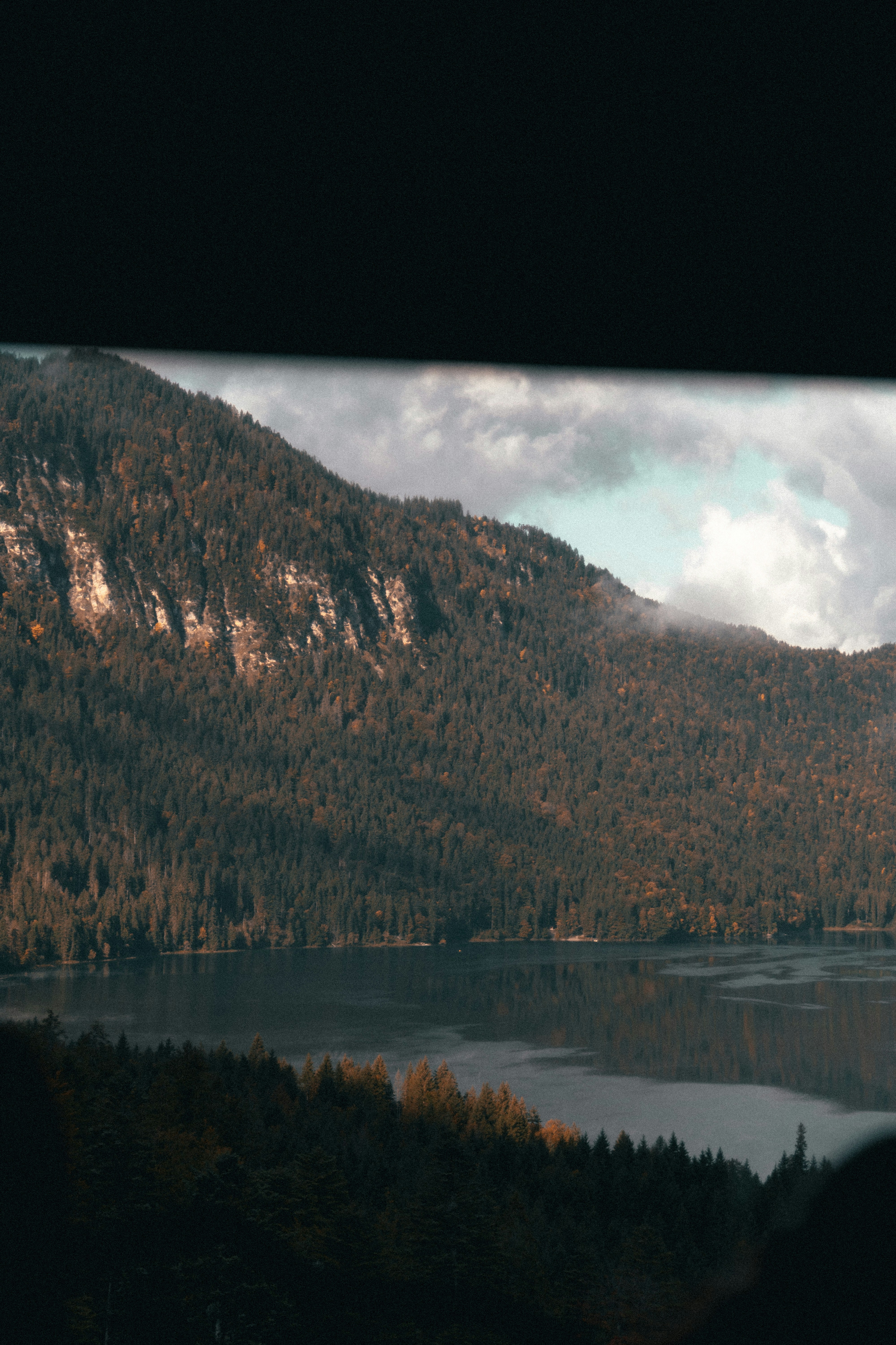 Lush green mountains reflect in a serene lake under a moody sky, showcasing nature's tranquility and beauty.