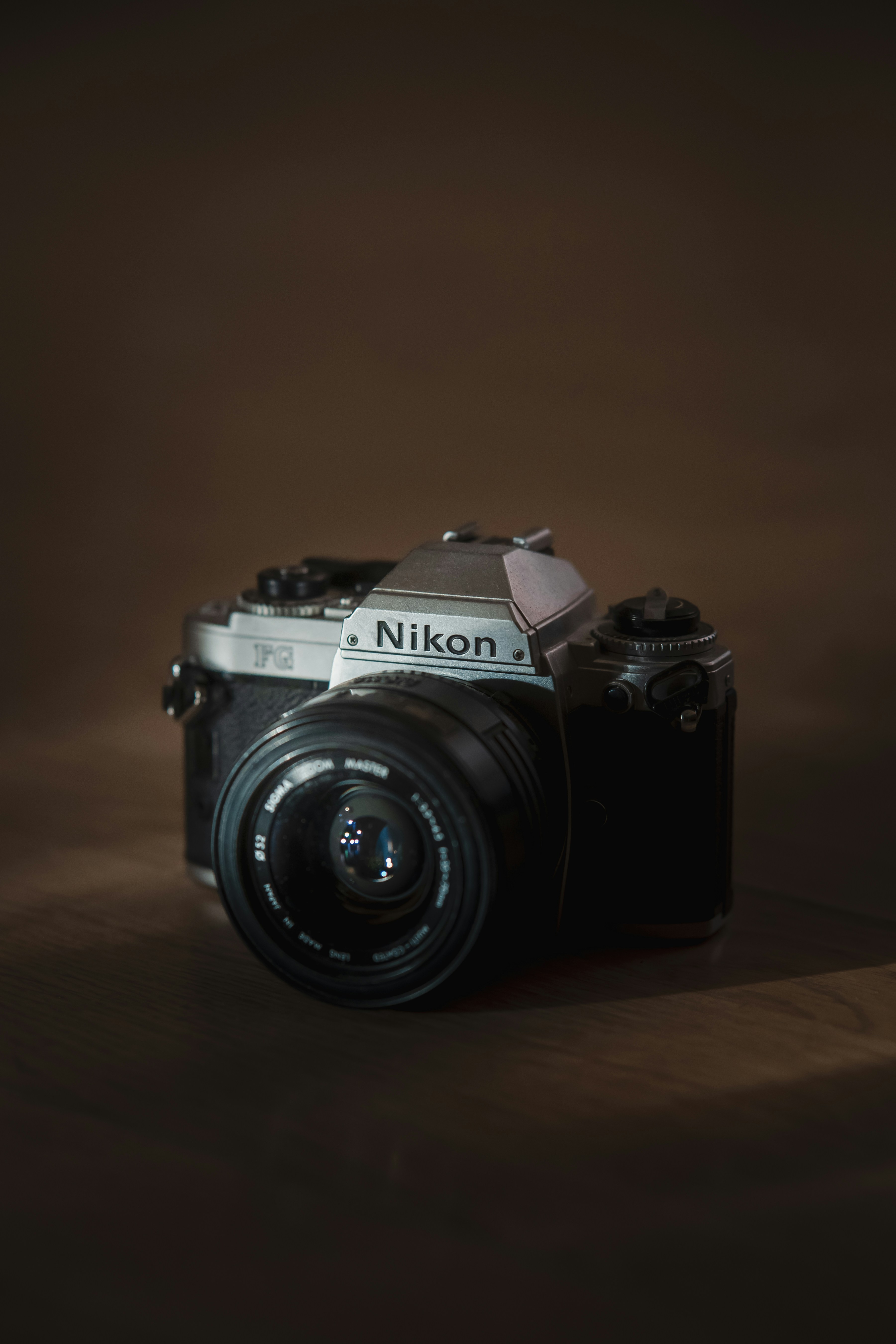 A Nikon camera positioned on a wooden surface, showcasing its classic design and lens details. The soft lighting highlights its vintage appeal.