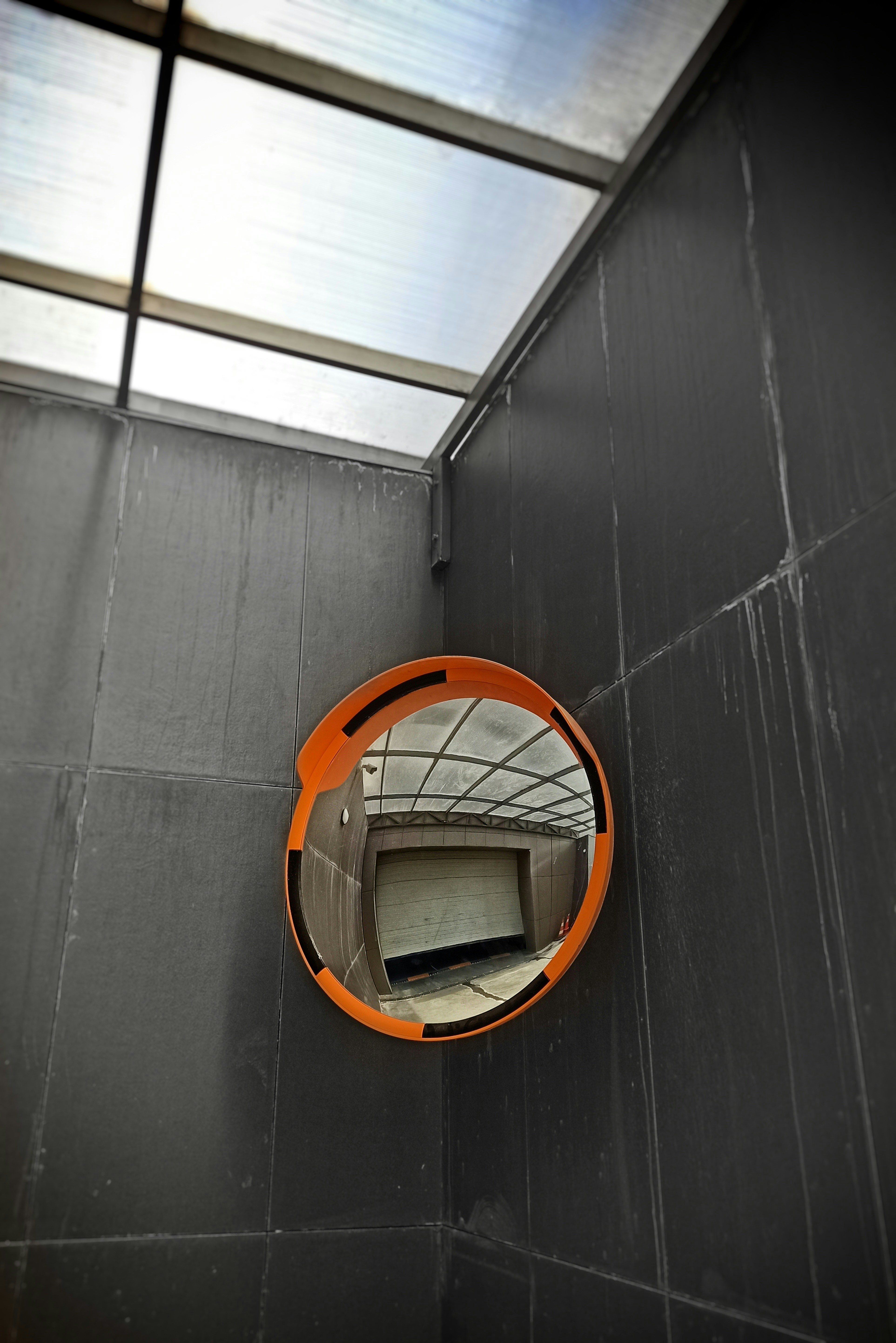 Orange circular mirror reflecting a minimalist interior with a black wall and skylight above.