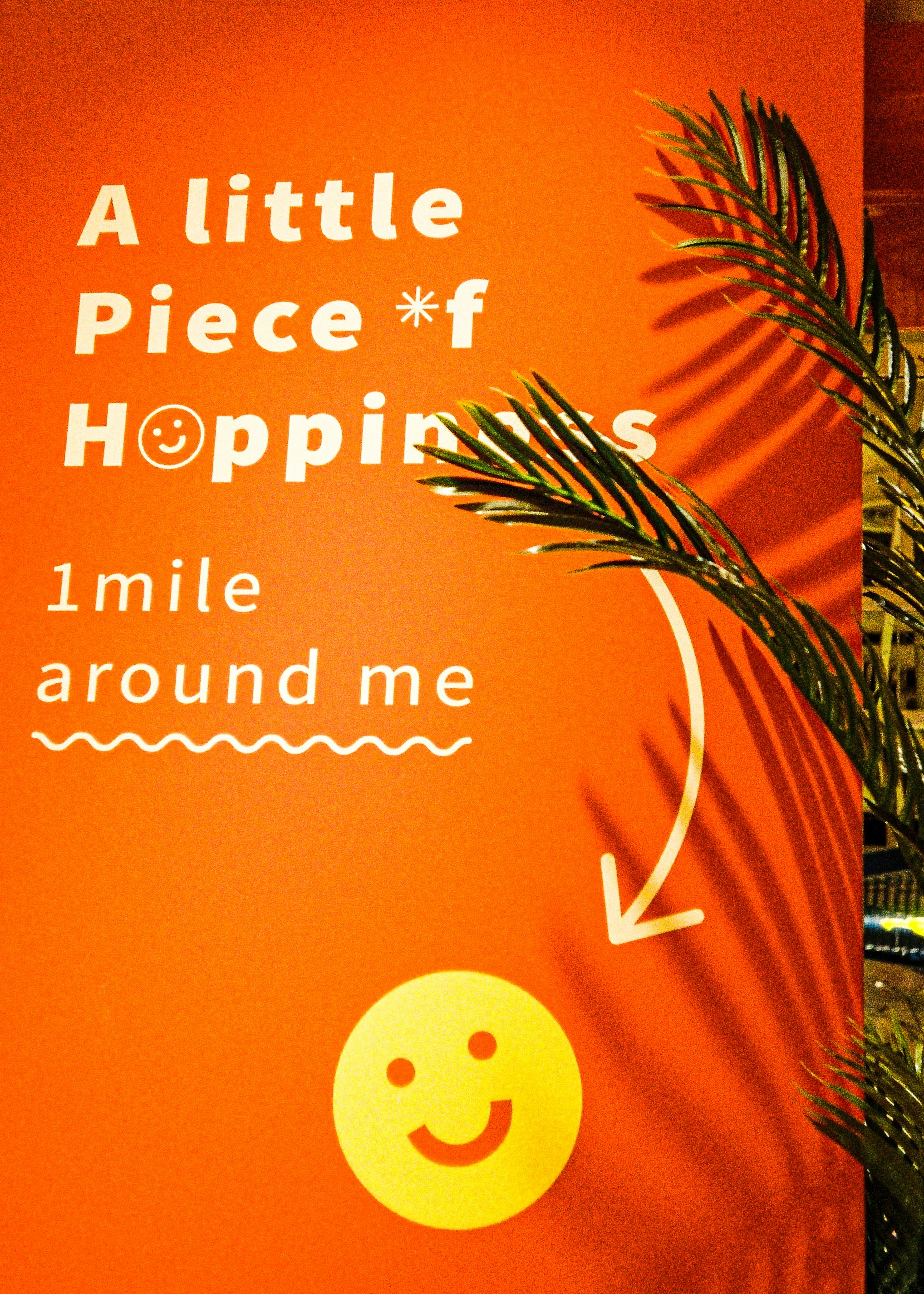 Bold orange poster with white text and a yellow smiley at the bottom, featuring an arrow and plant shadows in the background.