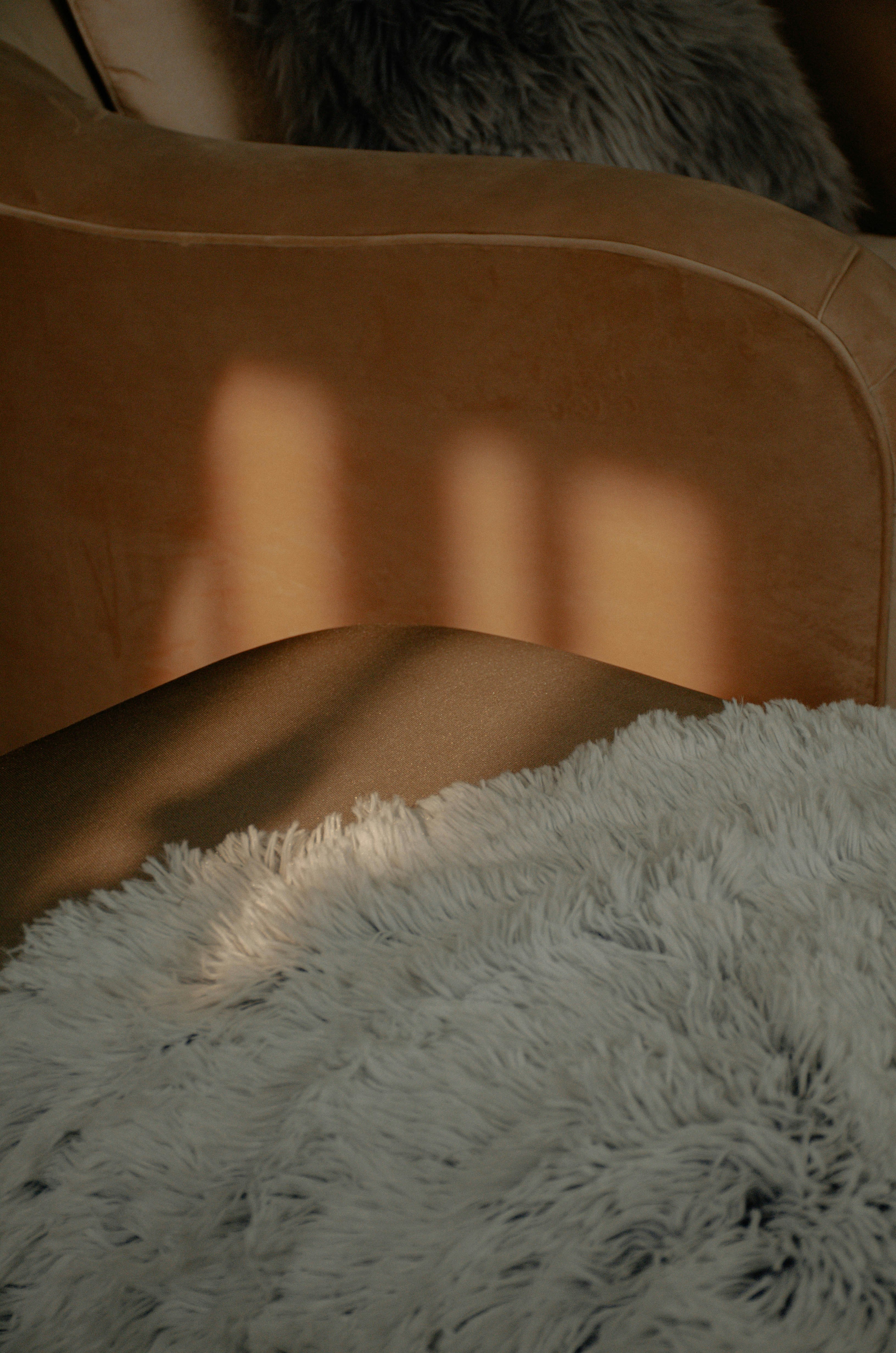 Soft, textured throw draped over a plush chair, illuminated by gentle sunlight filtering through nearby window slats.