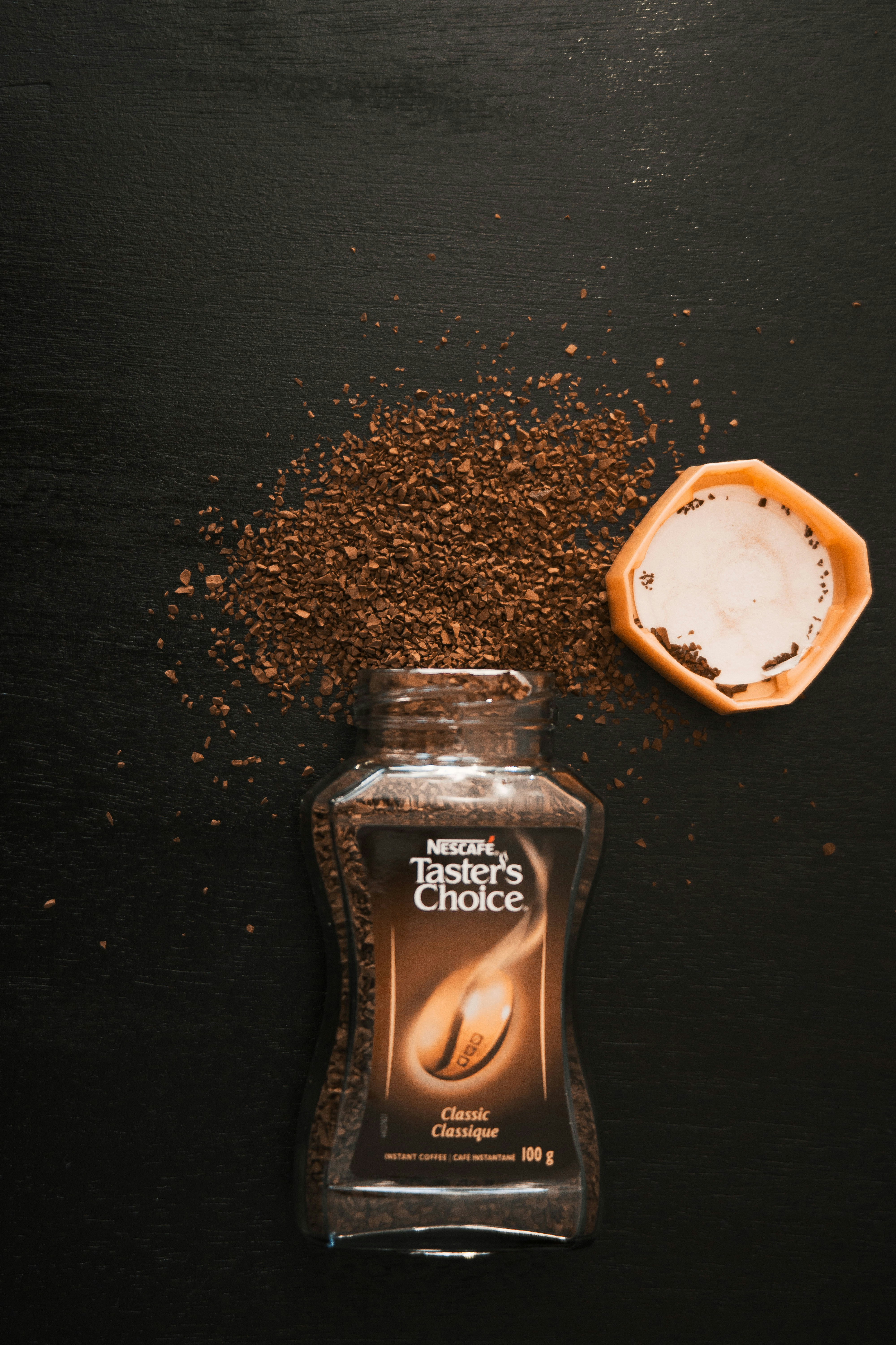 Instant coffee jar with spilled granules on a dark surface, highlighting the rich texture and aroma of the blend.