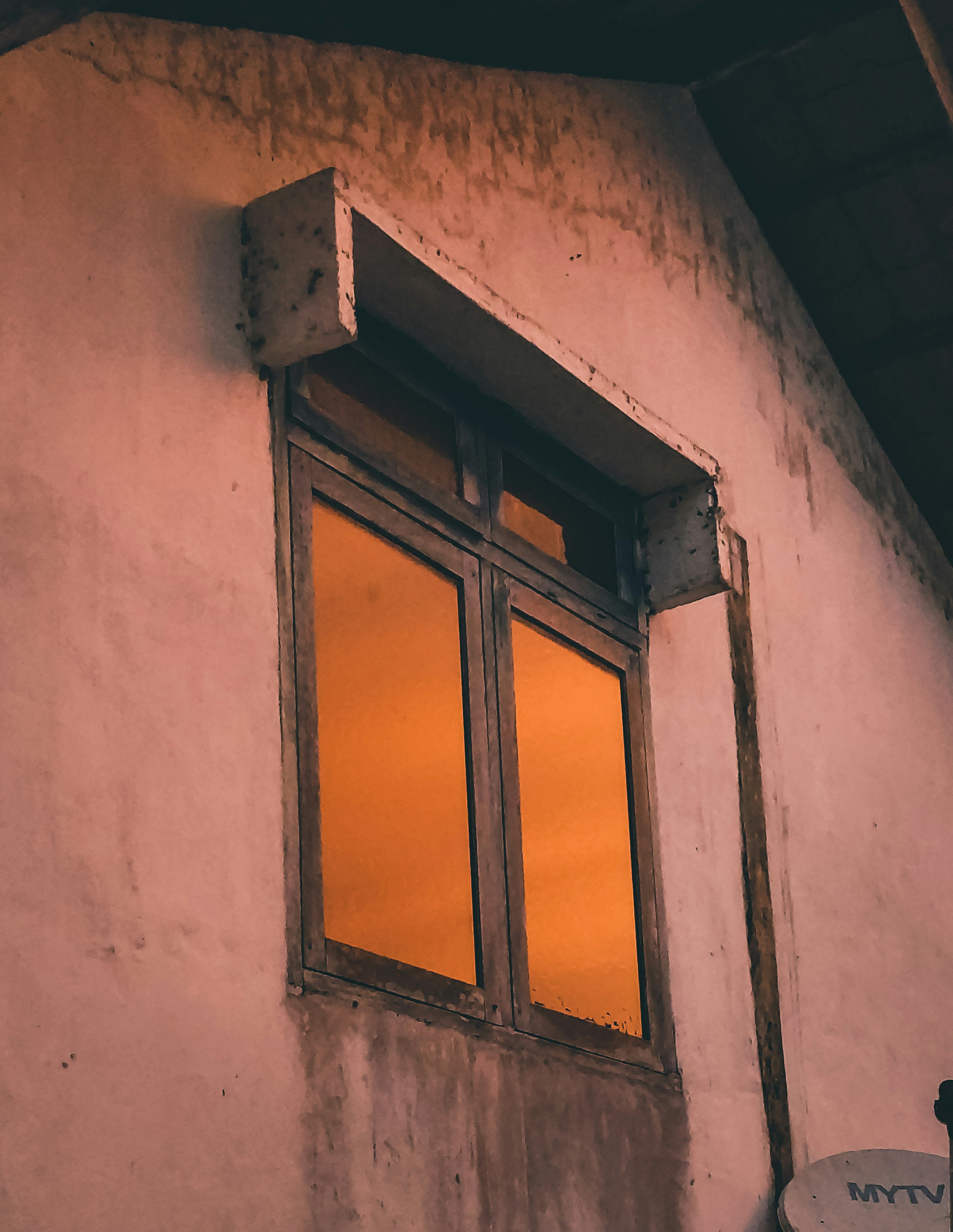 A weathered window framed against a softly glowing orange backdrop, hinting at the fading light of dusk.