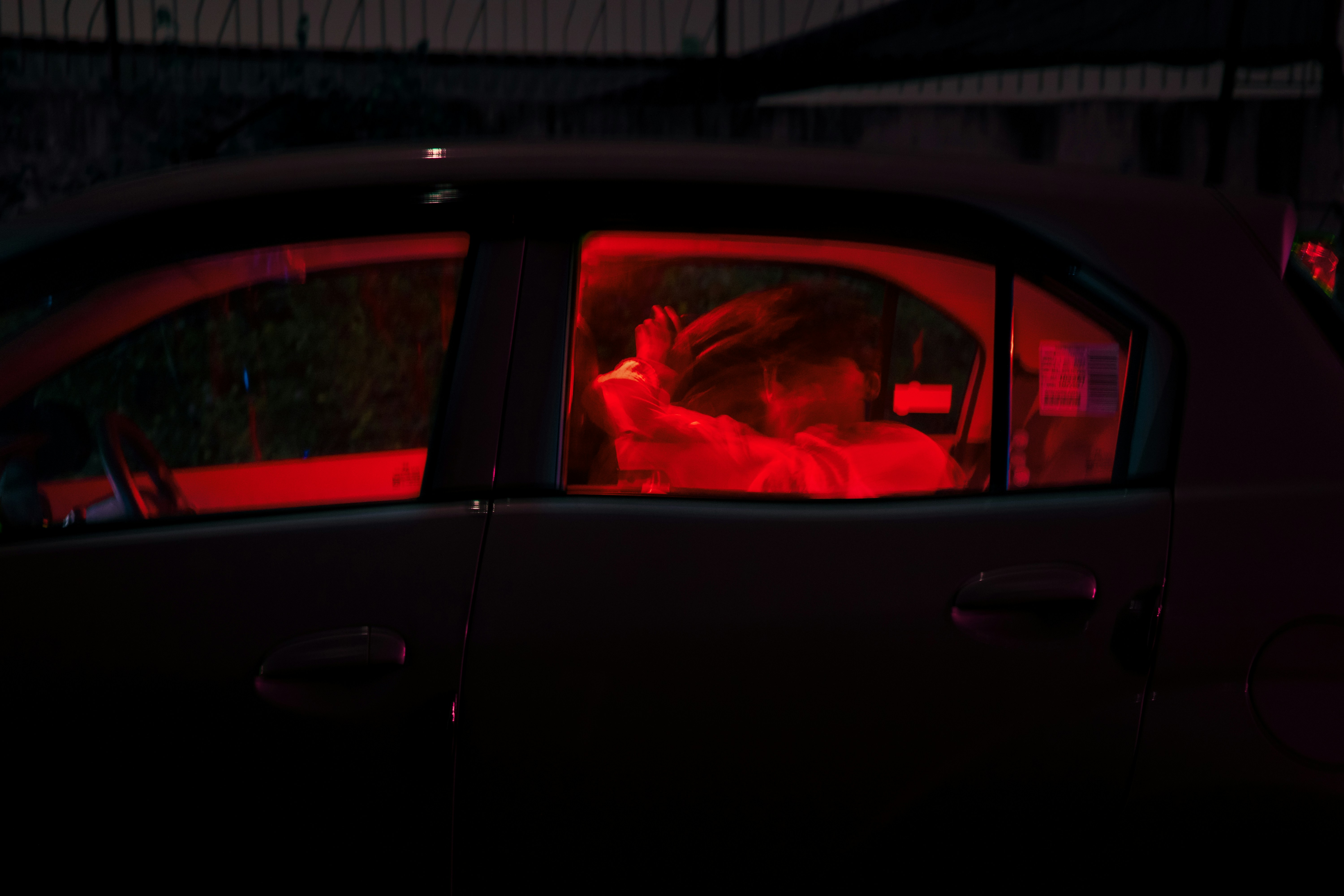 A couple sharing an intimate moment inside a car, illuminated by a striking red light. The scene captures the essence of closeness amidst urban shadows.