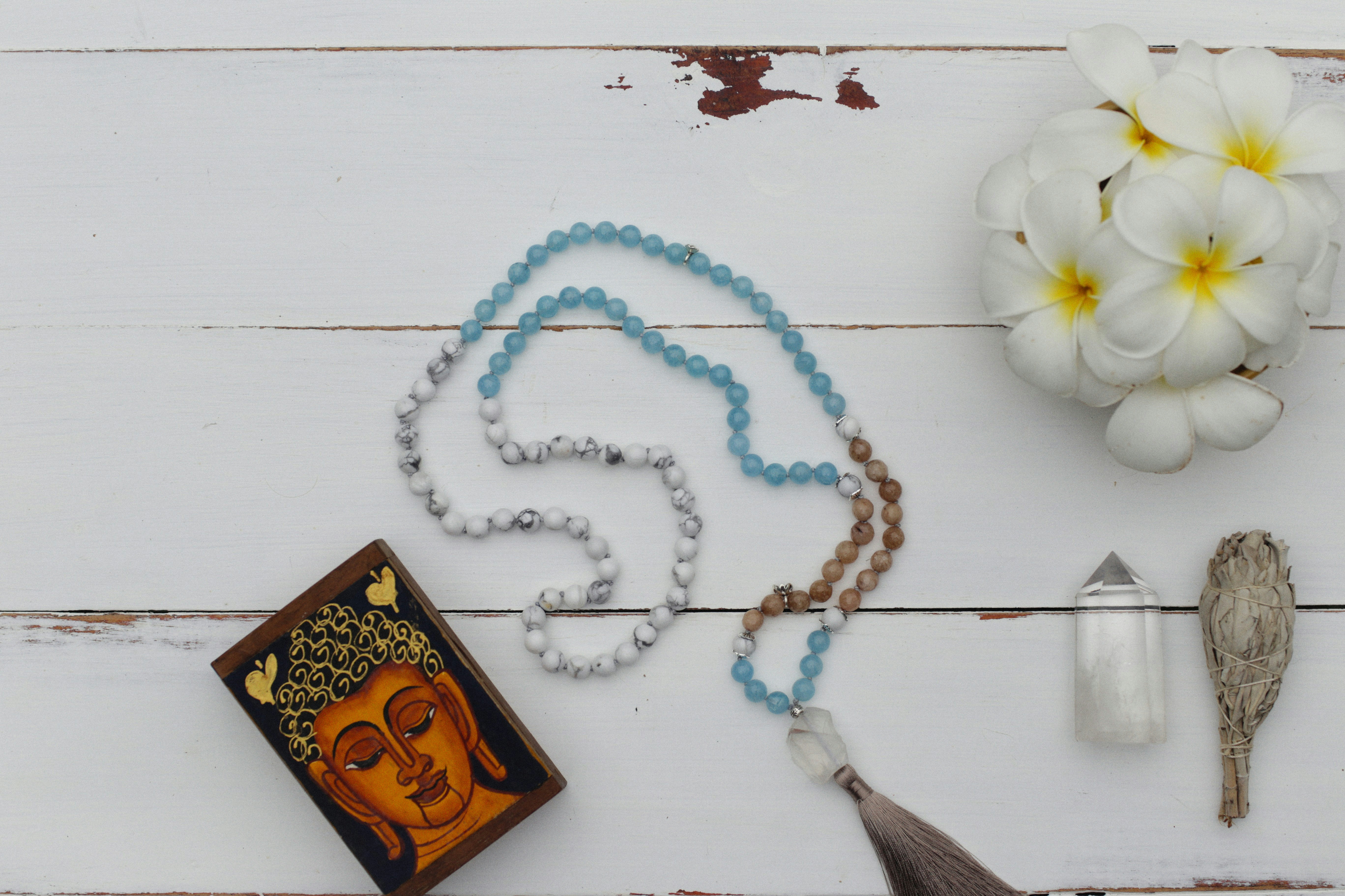 Beads, Buddha, and Plumeria: A Quiet Still-Life on White Wood