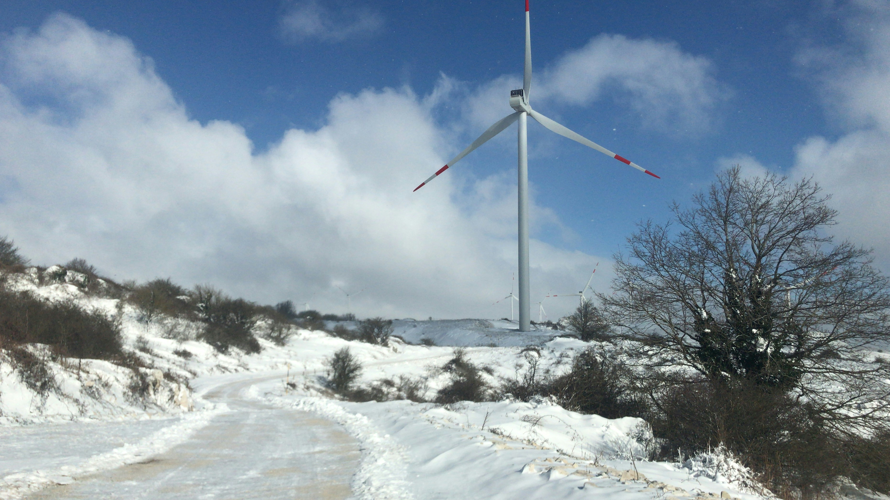 Wind turbine standing tall in a snow-covered landscape under a bright blue sky.
