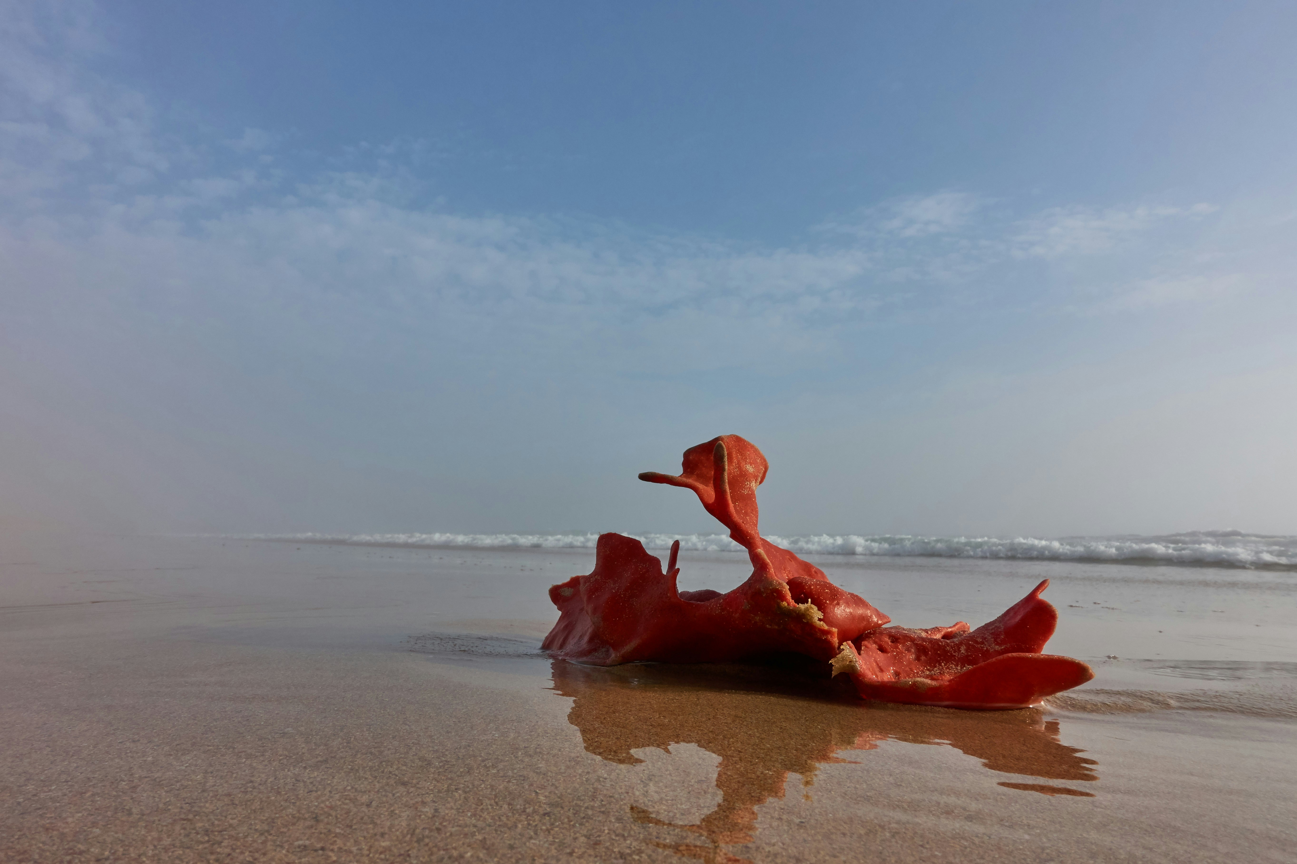 a piece of red plastic sitting on top of a sandy beach