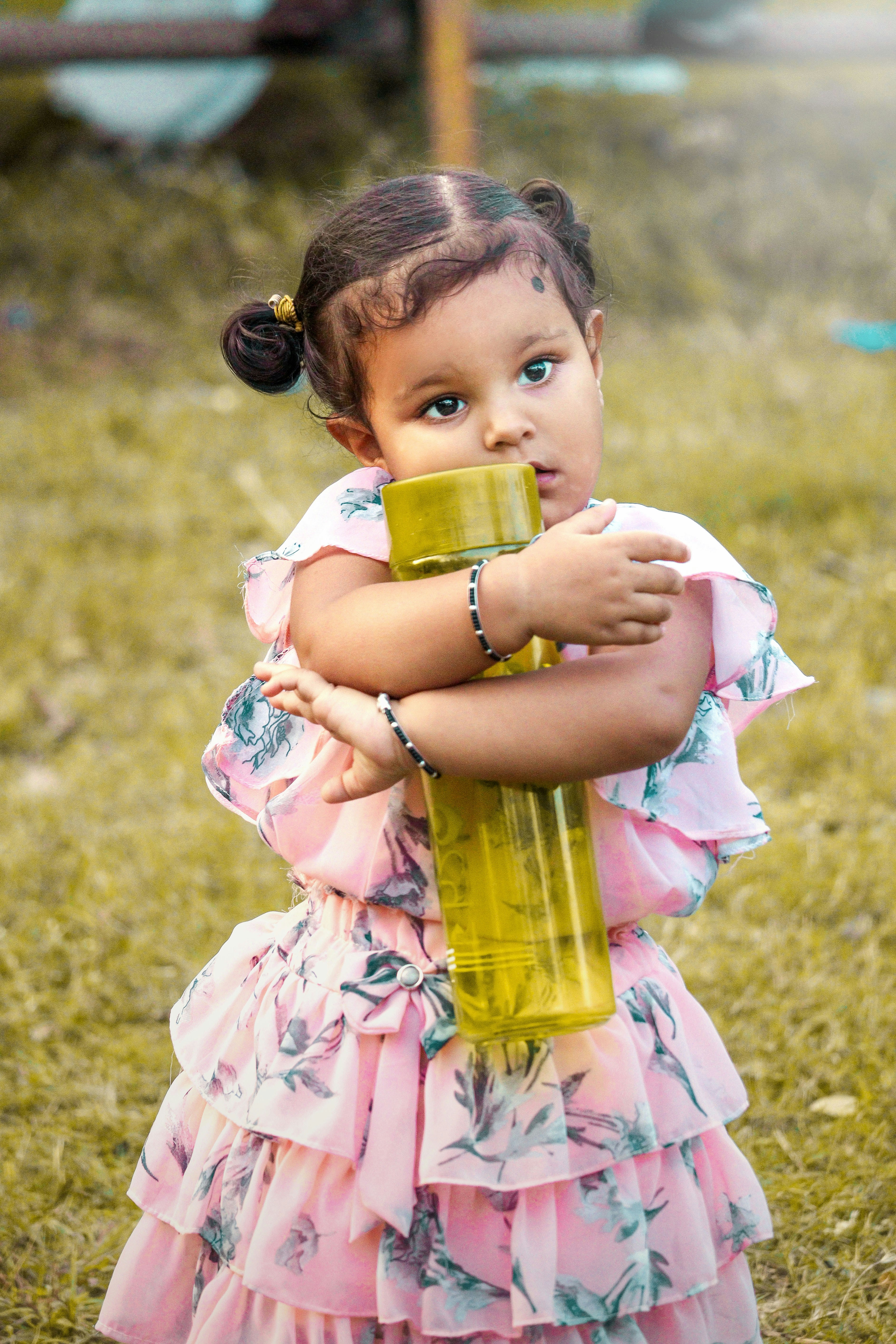 Pastel Embrace: A Little Girl in Floral Pink Holds a Sunny Yellow Bottle