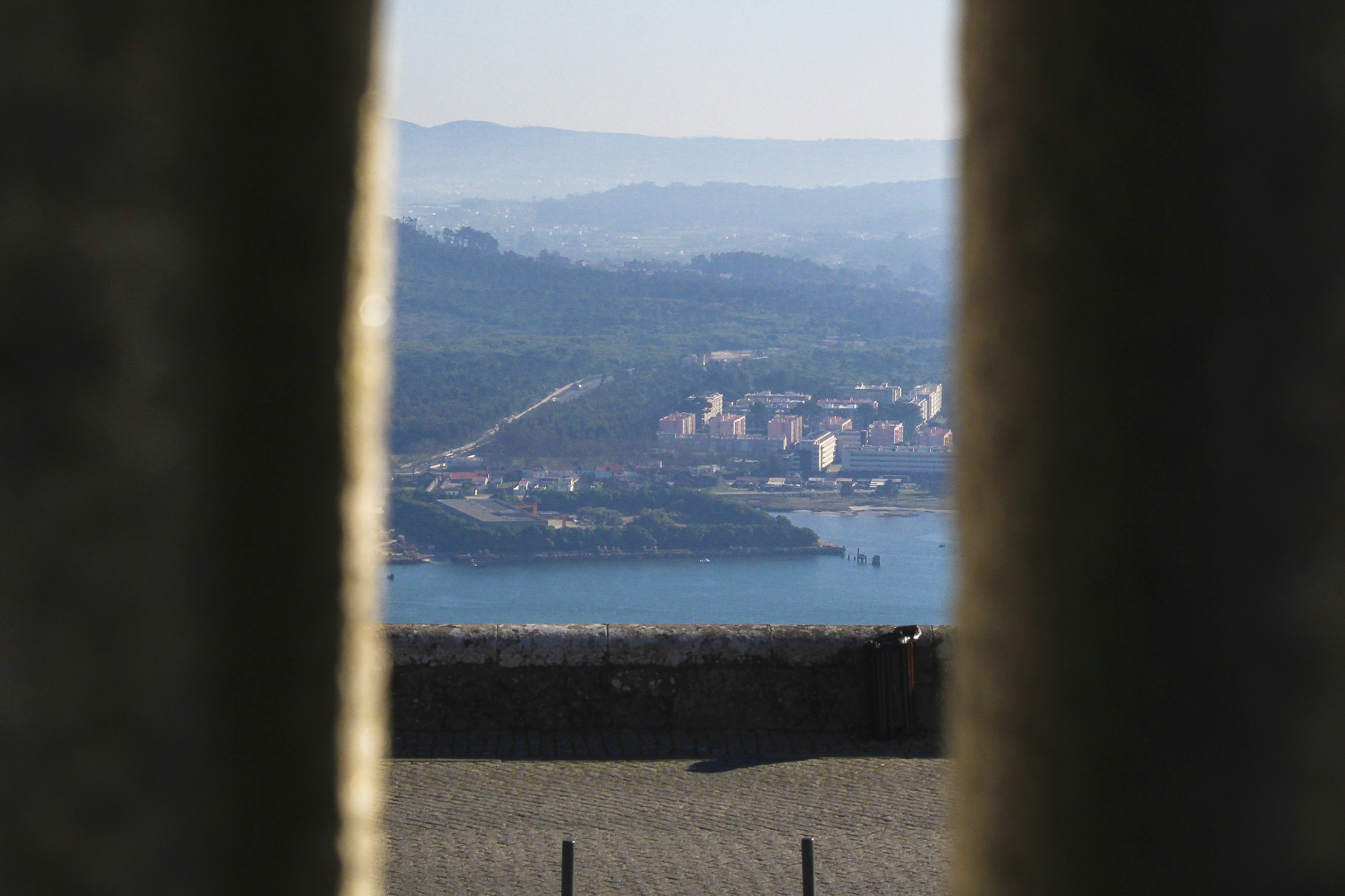 City view through a narrow gap between two stone pillars with water and distant hills in the background.
