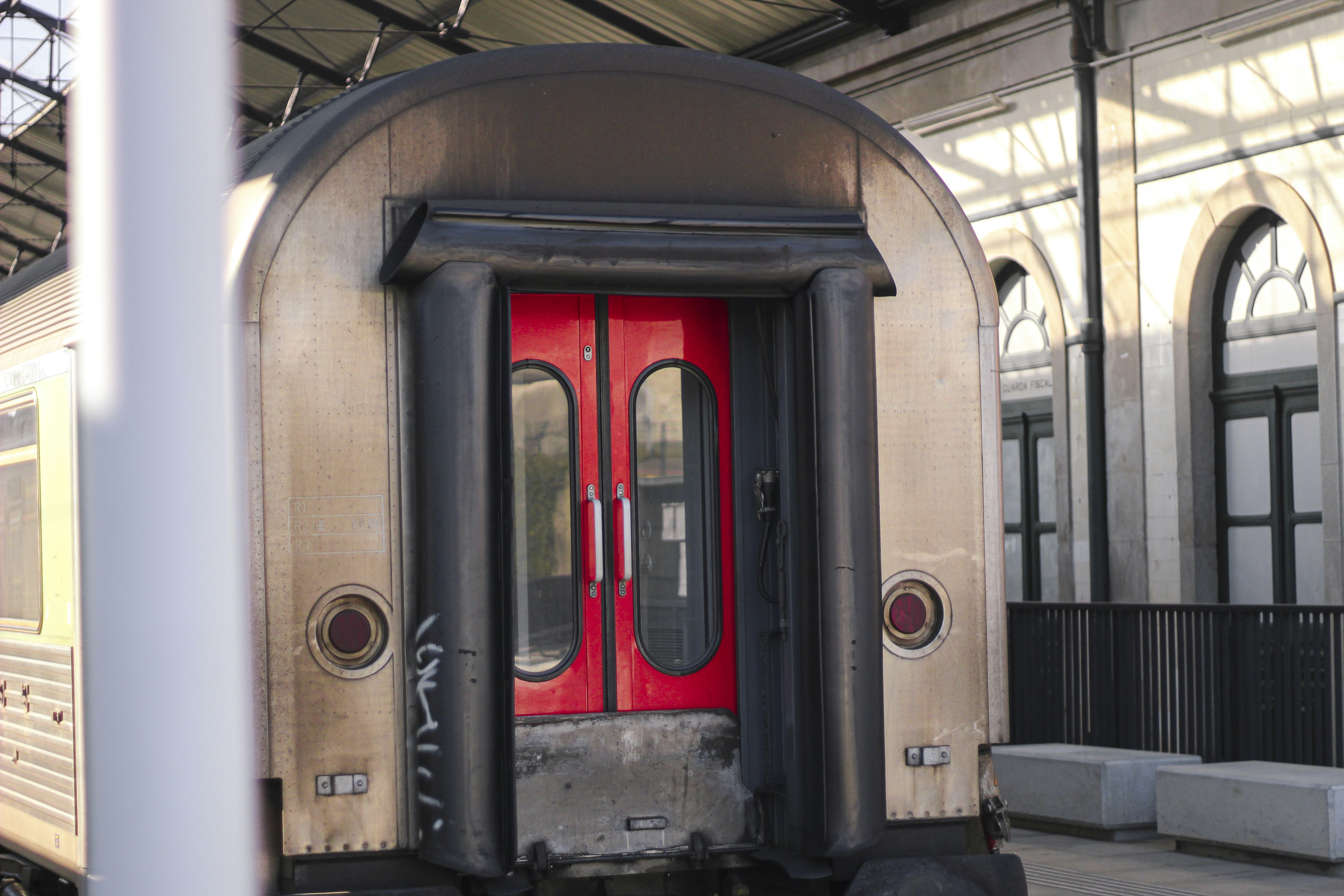 The rear view of an old train carriage with striking red doors, set against a backdrop of architectural details at a train station.