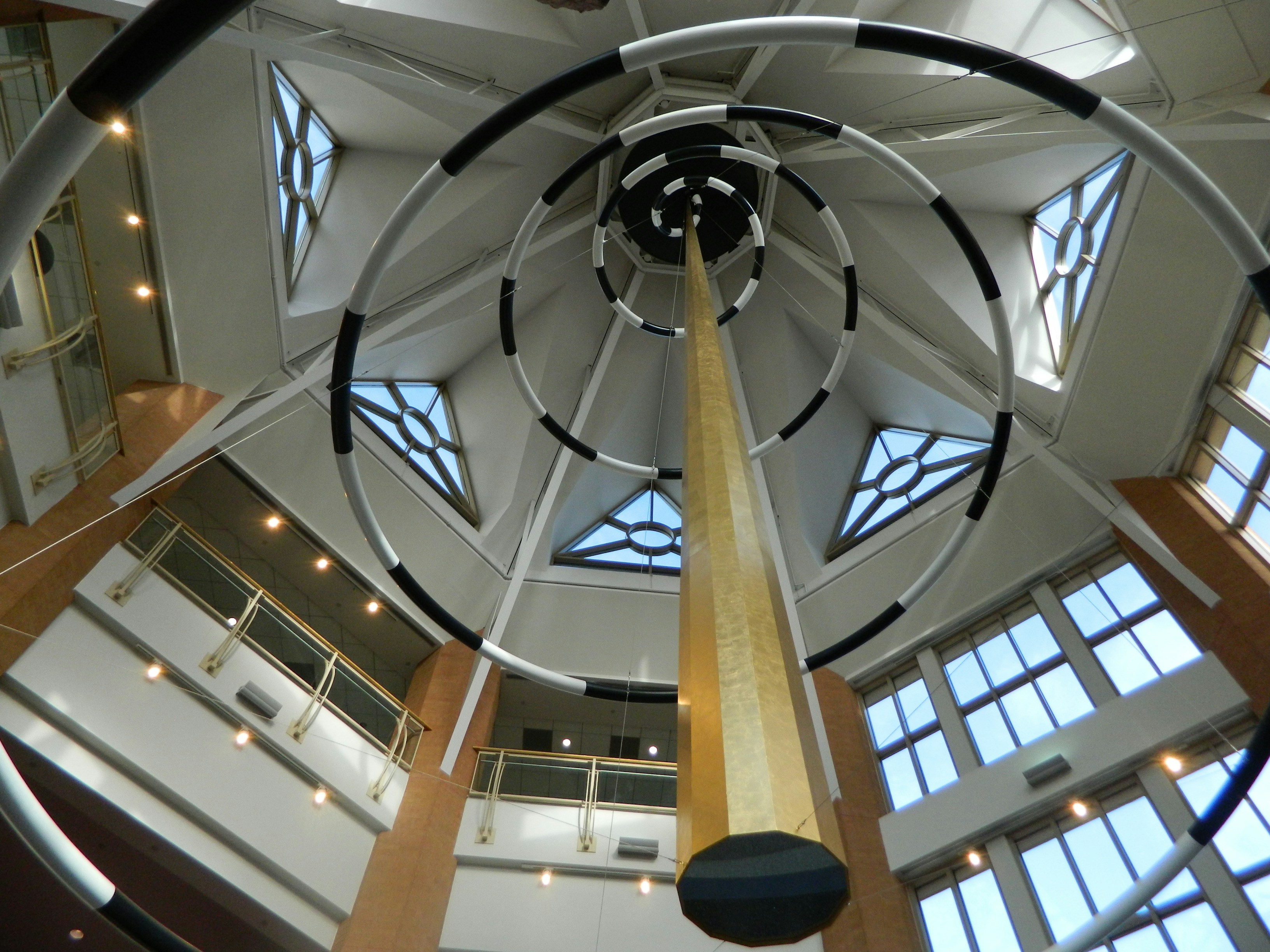 A striking view from below, showcasing a spiral structure with a golden pillar and geometric ceiling patterns in a modern atrium.