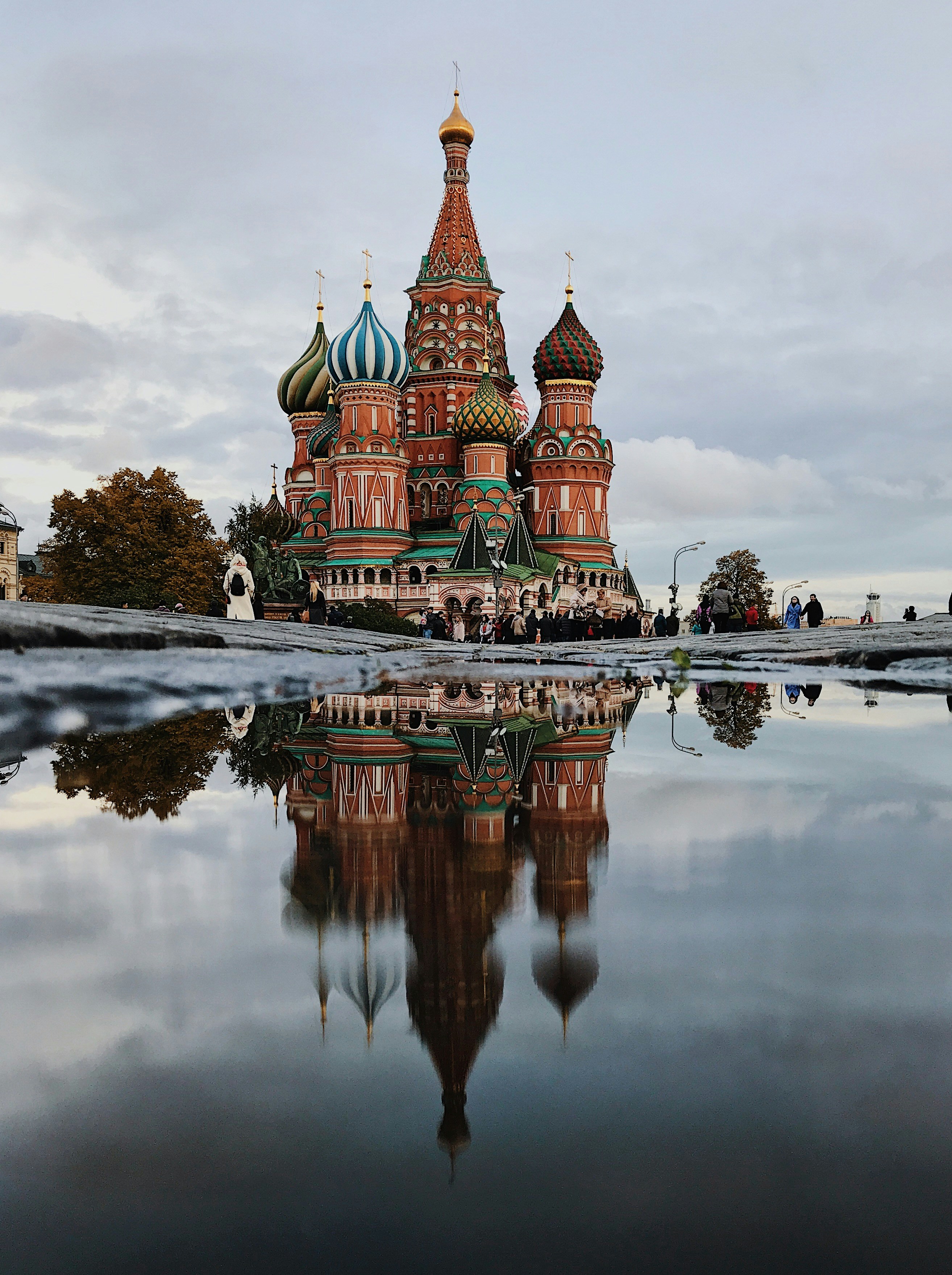 St. Basil's Cathedral stands majestically, its vibrant domes mirrored in a puddle at sunset. The scene captures the essence of Moscow's architectural beauty.