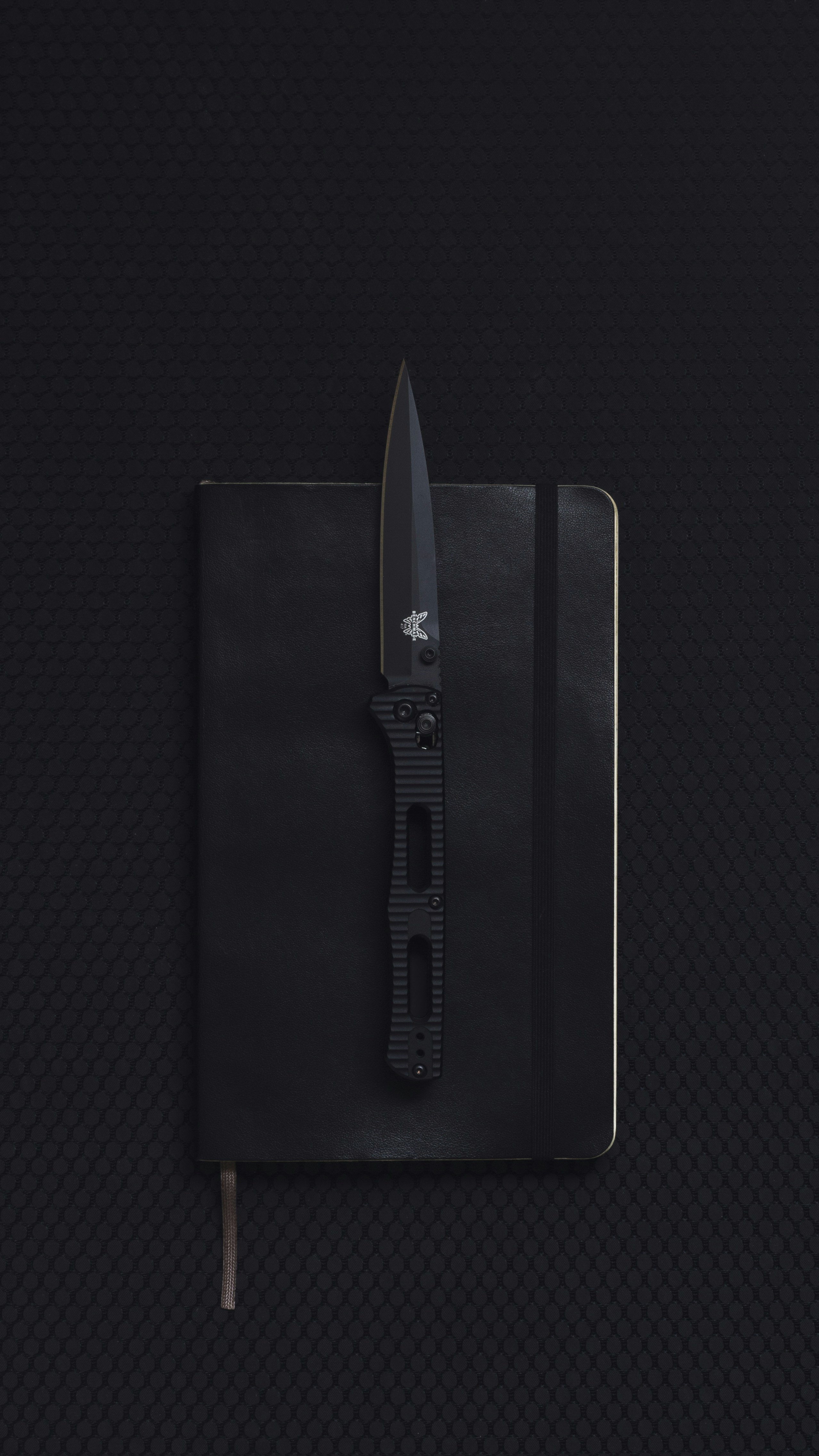 A sleek black knife rests atop a dark notebook, showcasing a minimalist aesthetic. The contrasting textures emphasize the craftsmanship of the knife.