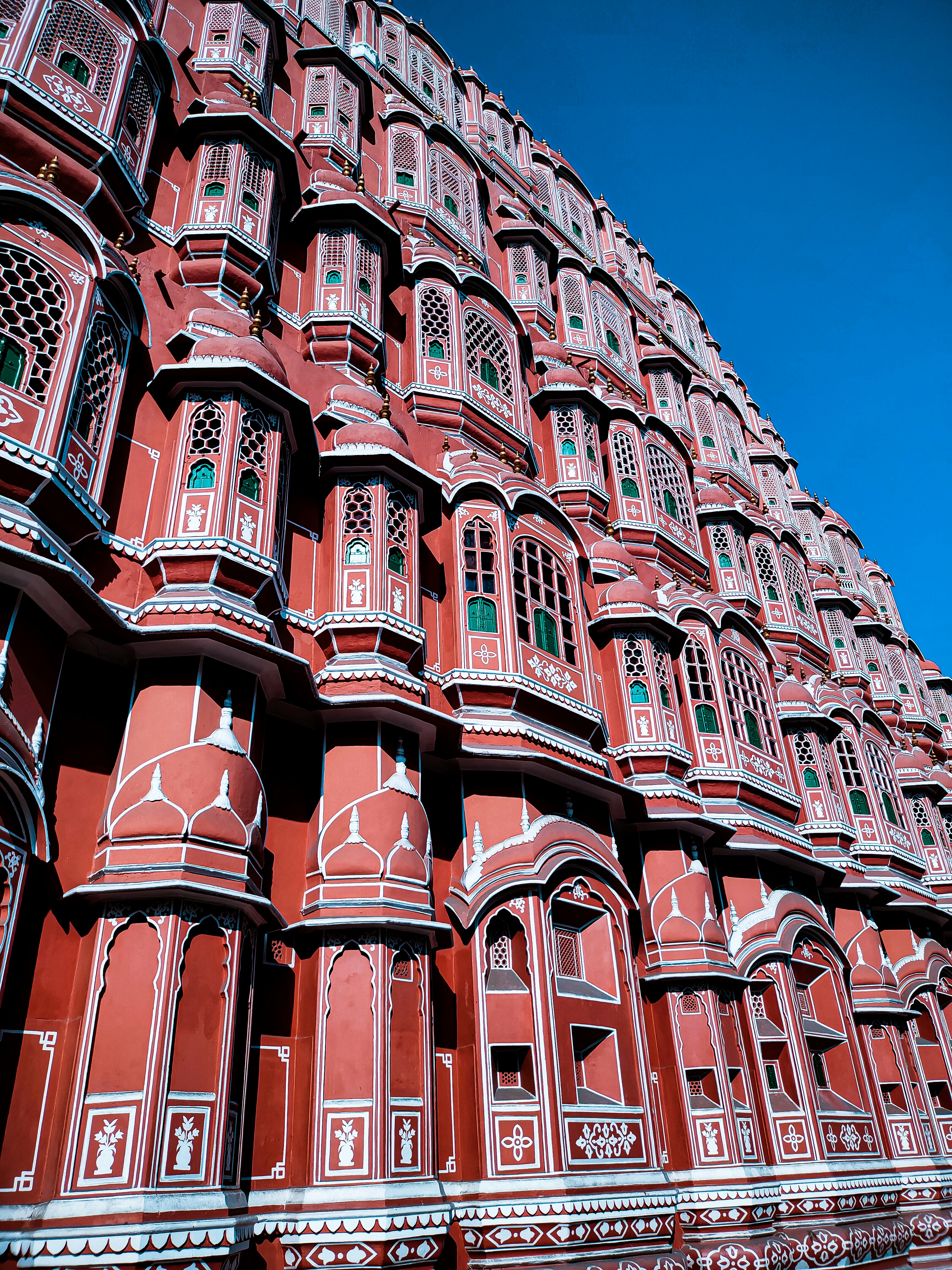 Photograph of Jaipur's Hawa Mahal red façade with intricate jharokha windows framed against a vibrant blue sky.