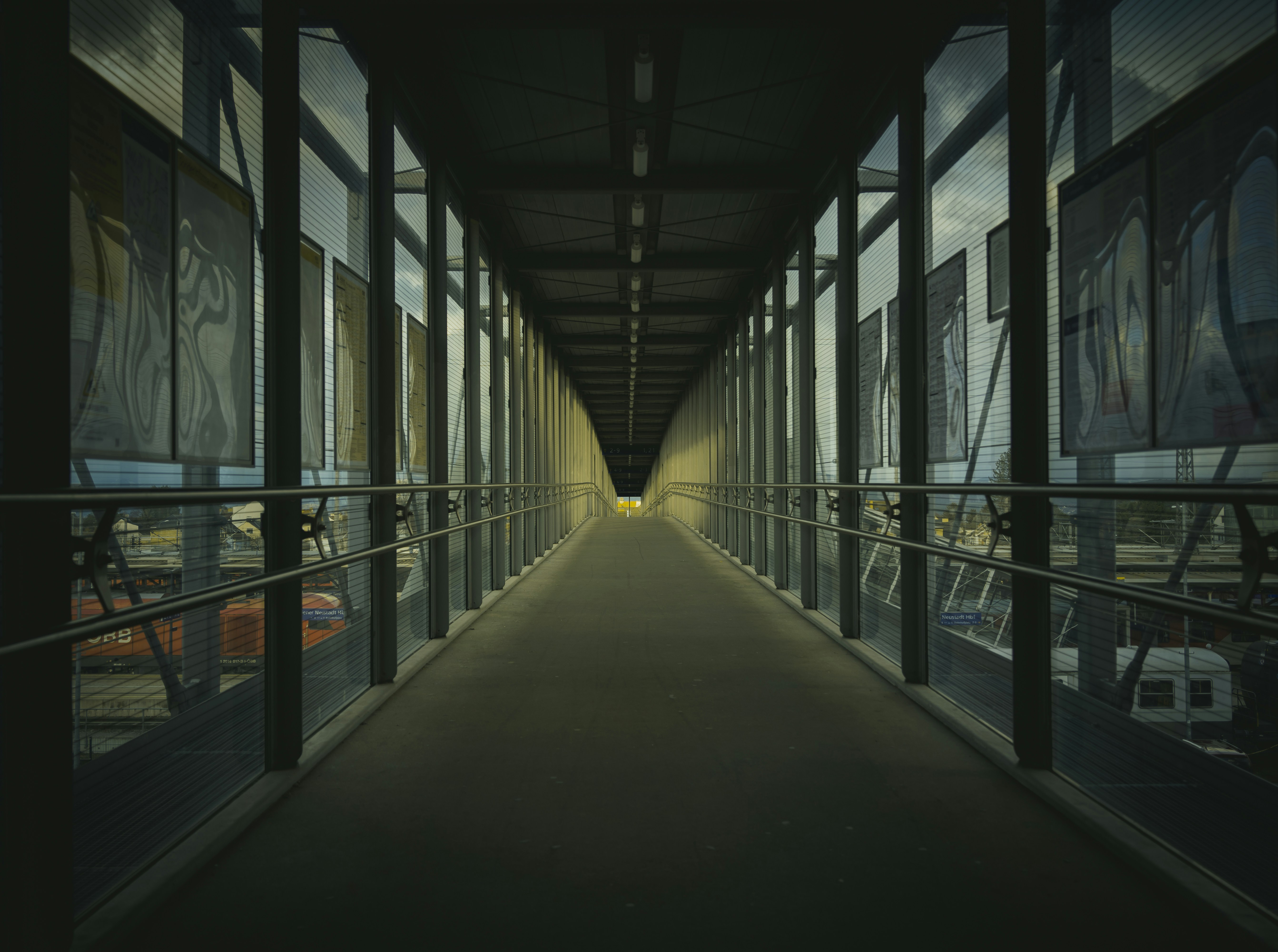 A sleek, modern walkway framed by glass panels, leading towards a bright exit, showcasing urban architecture.