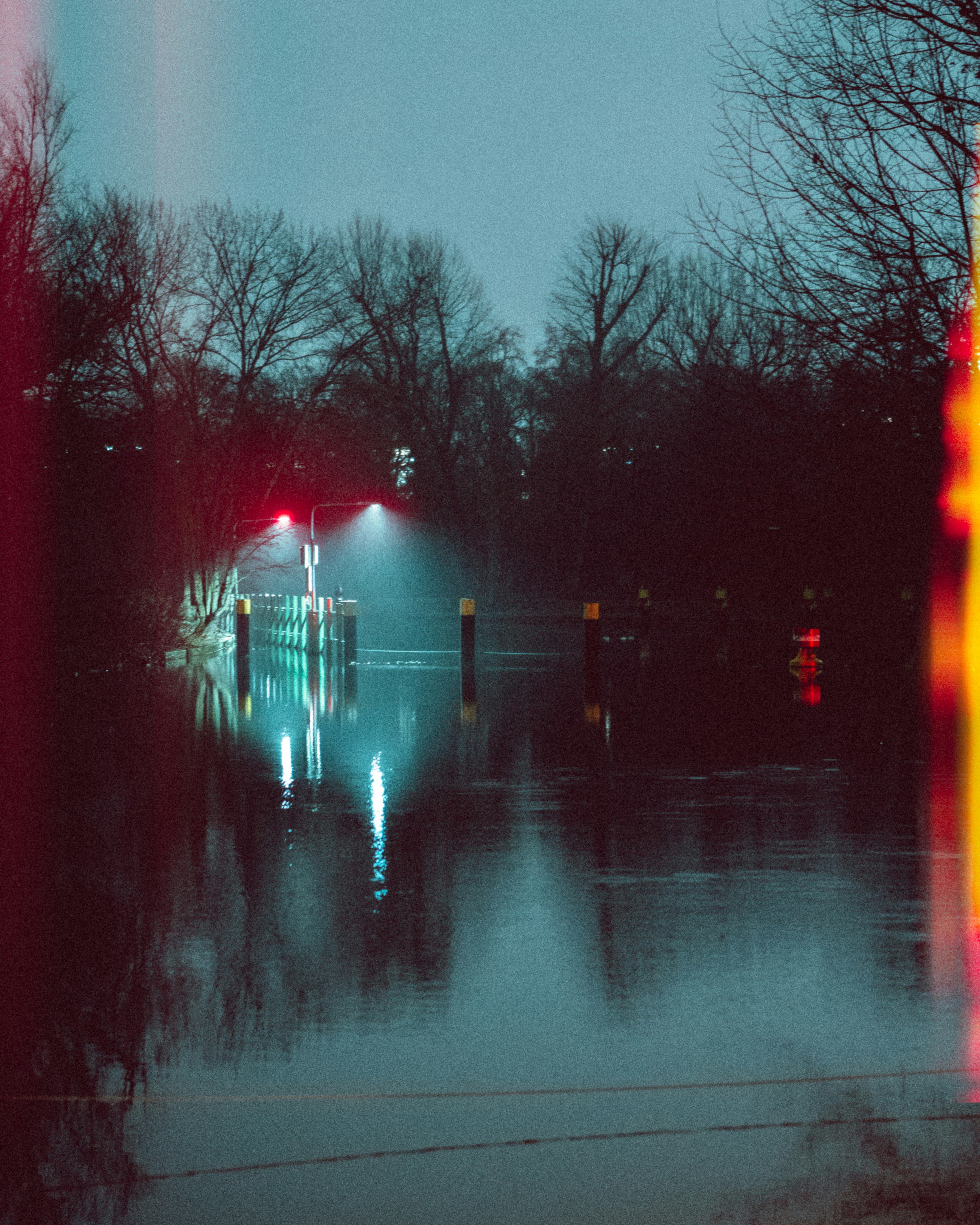 A serene night scene featuring glowing streetlights illuminating a calm waterway, surrounded by silhouetted trees. The reflections create a tranquil atmosphere.