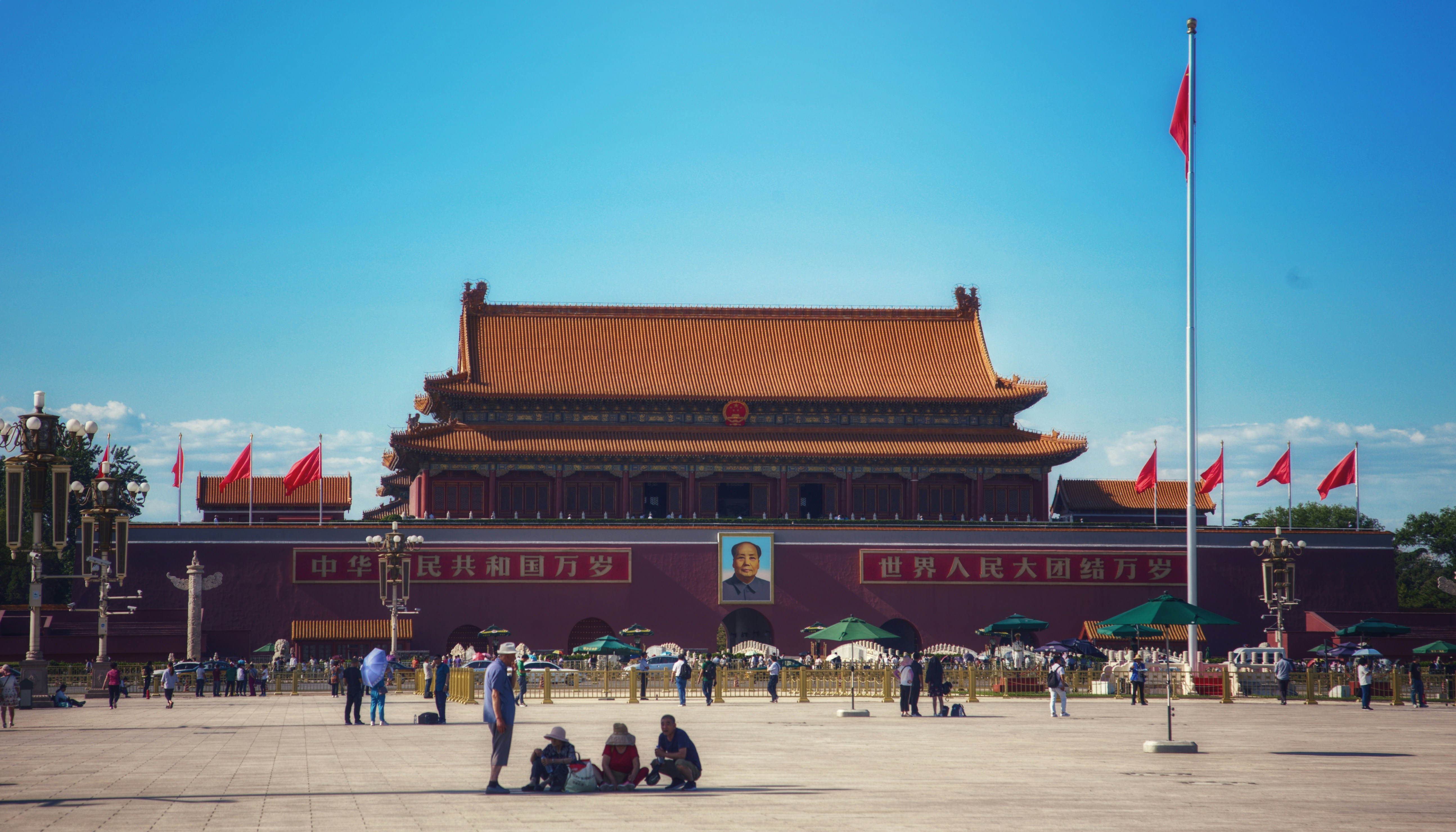 Historic building with red walls and a golden roof in a vast public square under a clear blue sky.