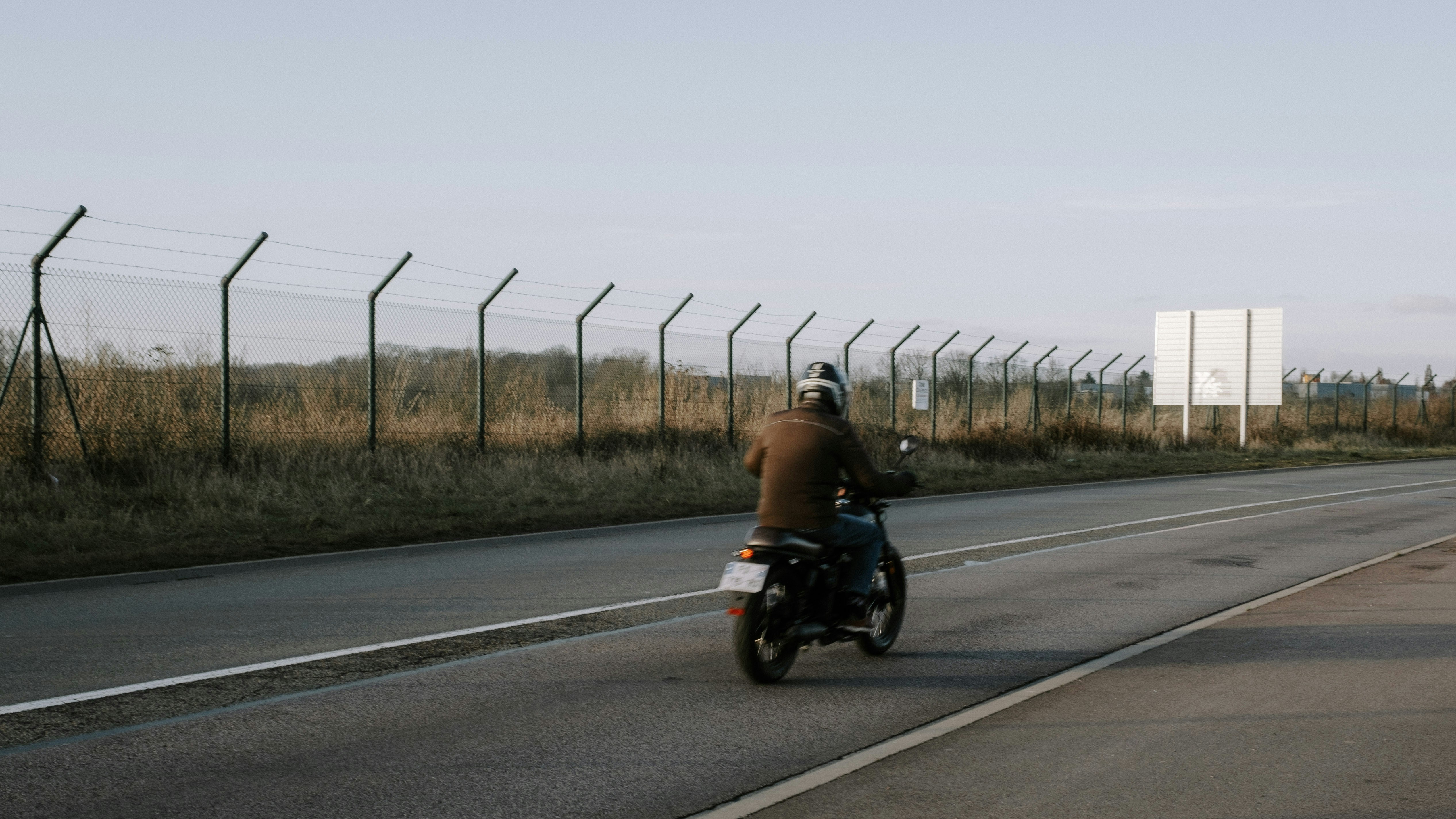 A man riding a motorcycle down a road next to a barbed wire fence photo ...