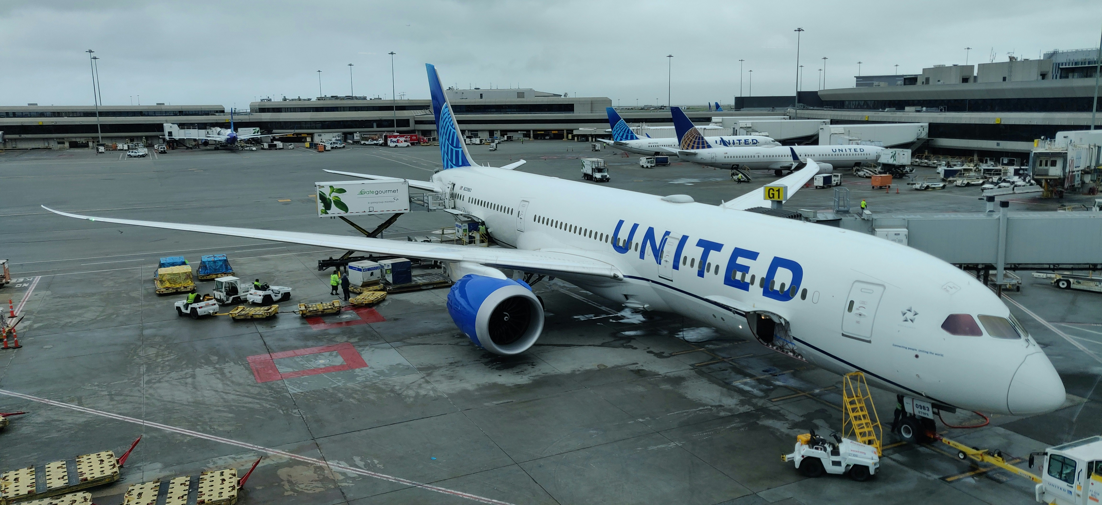 United Airlines Boeing 787 parked at the airport, surrounded by ground service vehicles and other aircraft. The scene captures the bustling atmosphere of air travel.