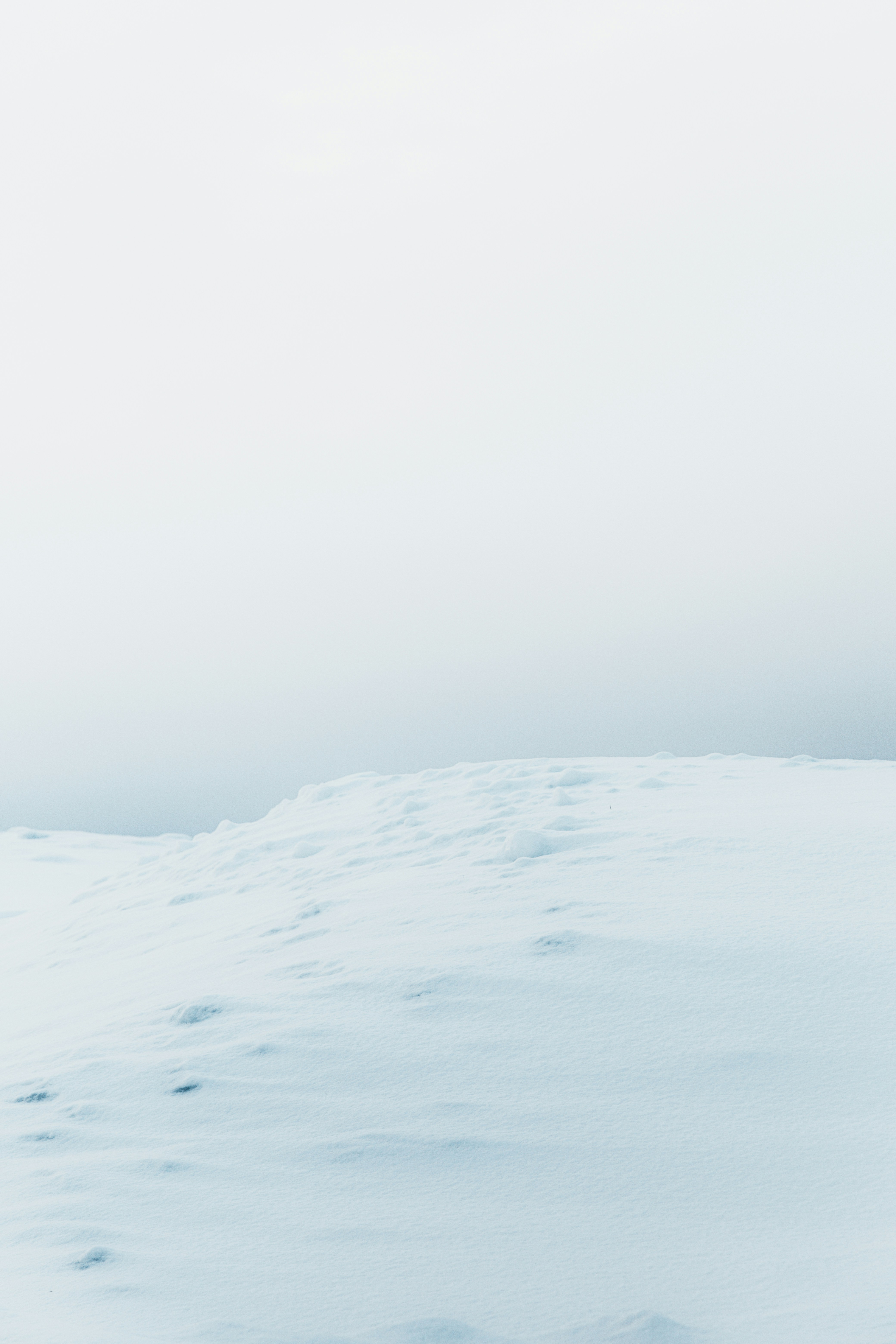 Soft, undulating snowdrifts blend seamlessly into a pale, misty horizon, evoking a serene winter landscape.