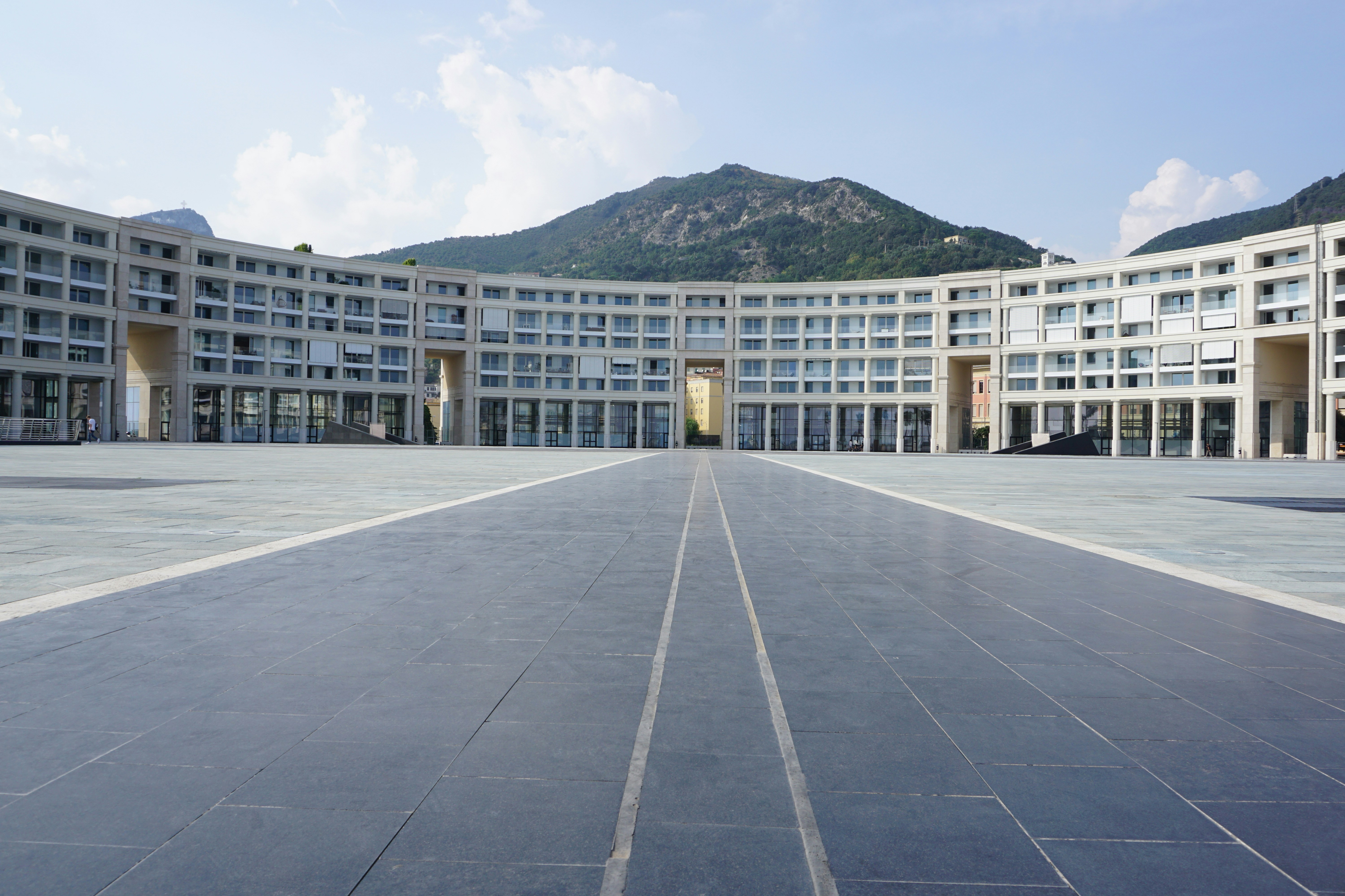 Curved building facade with arched windows and mountain backdrop under a clear sky.