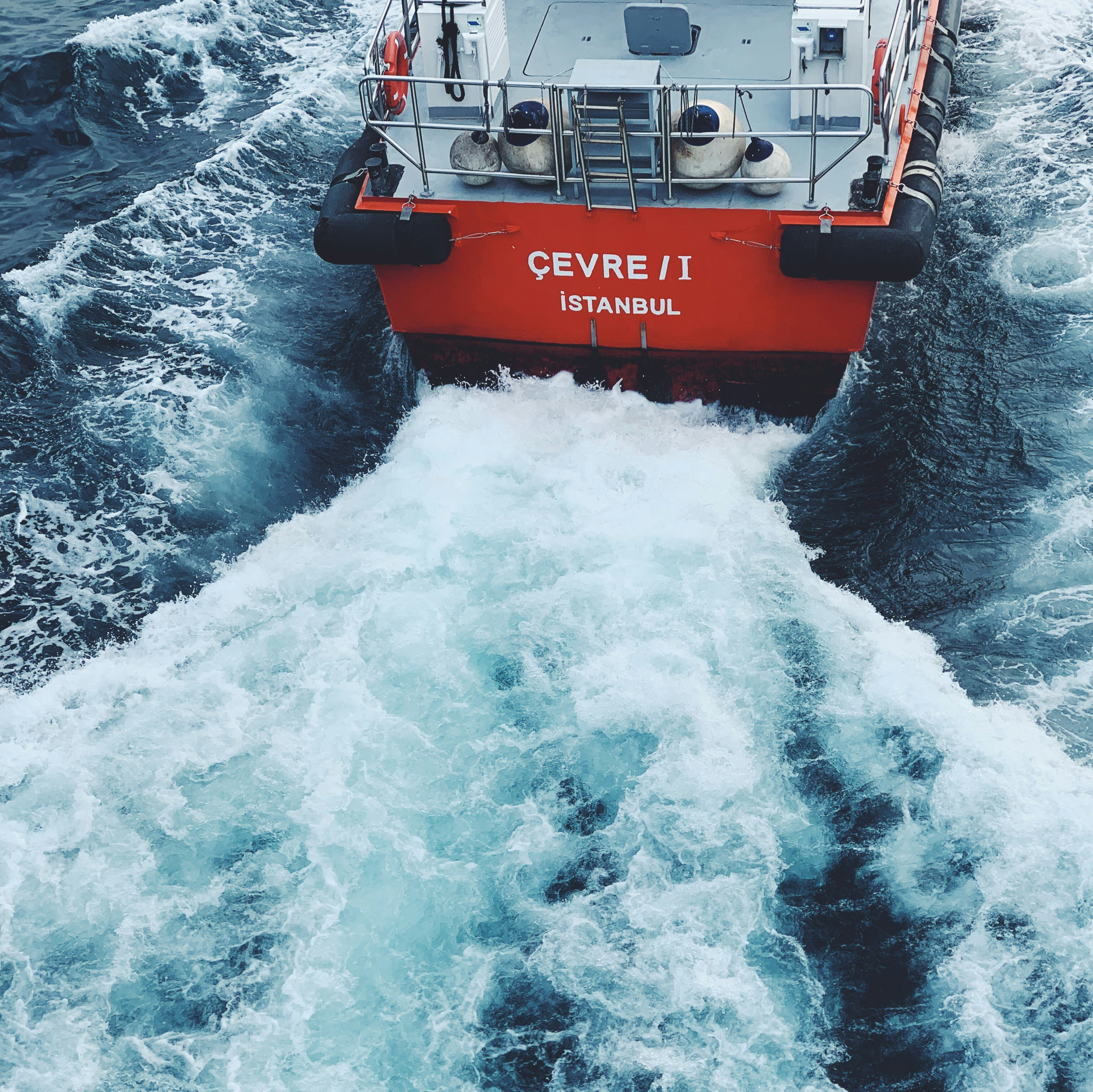 Red service boat carving a turquoise wake off Istanbul