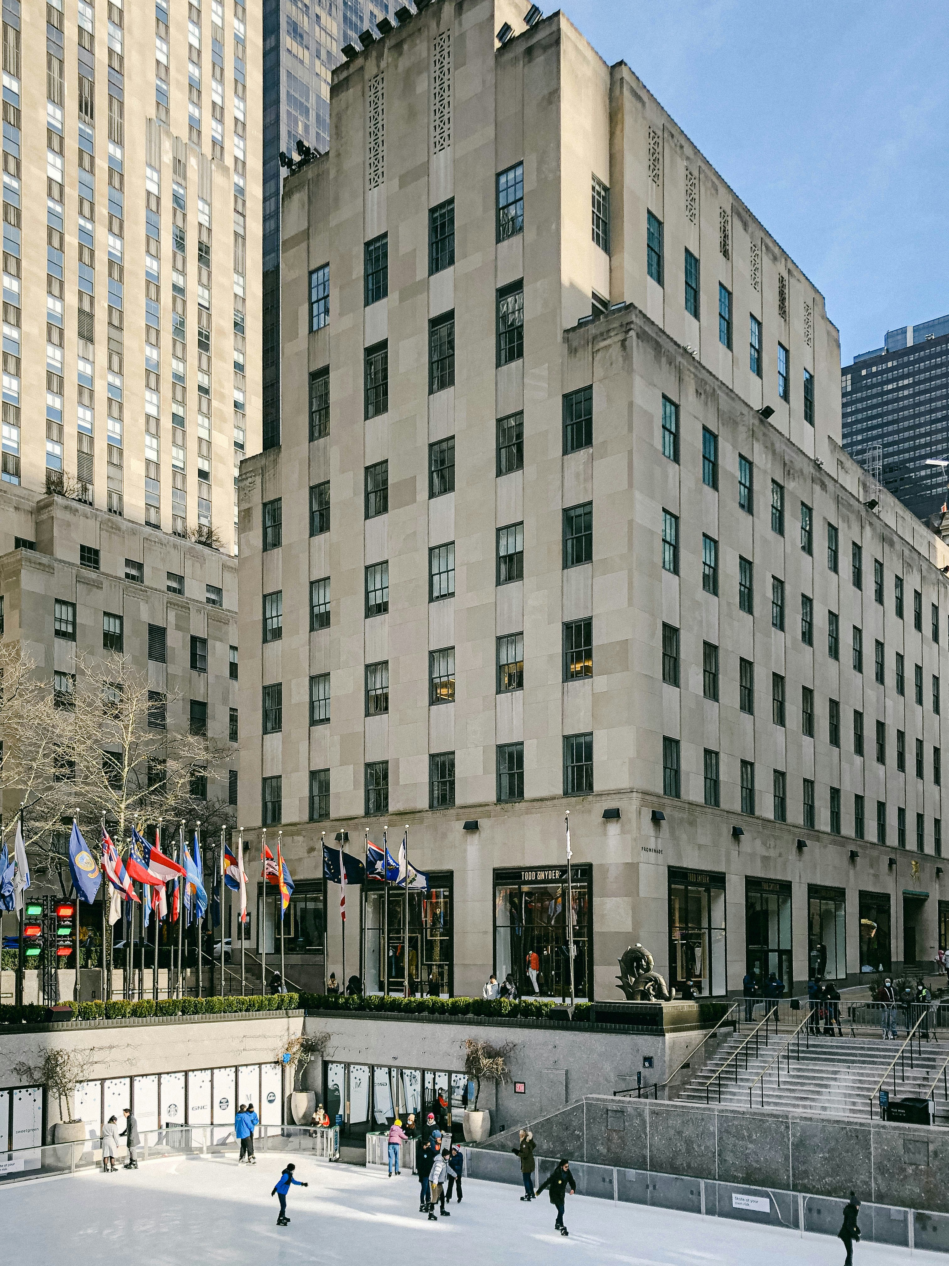 Flag-lined plaza and stone-faced office block under a bright blue sky